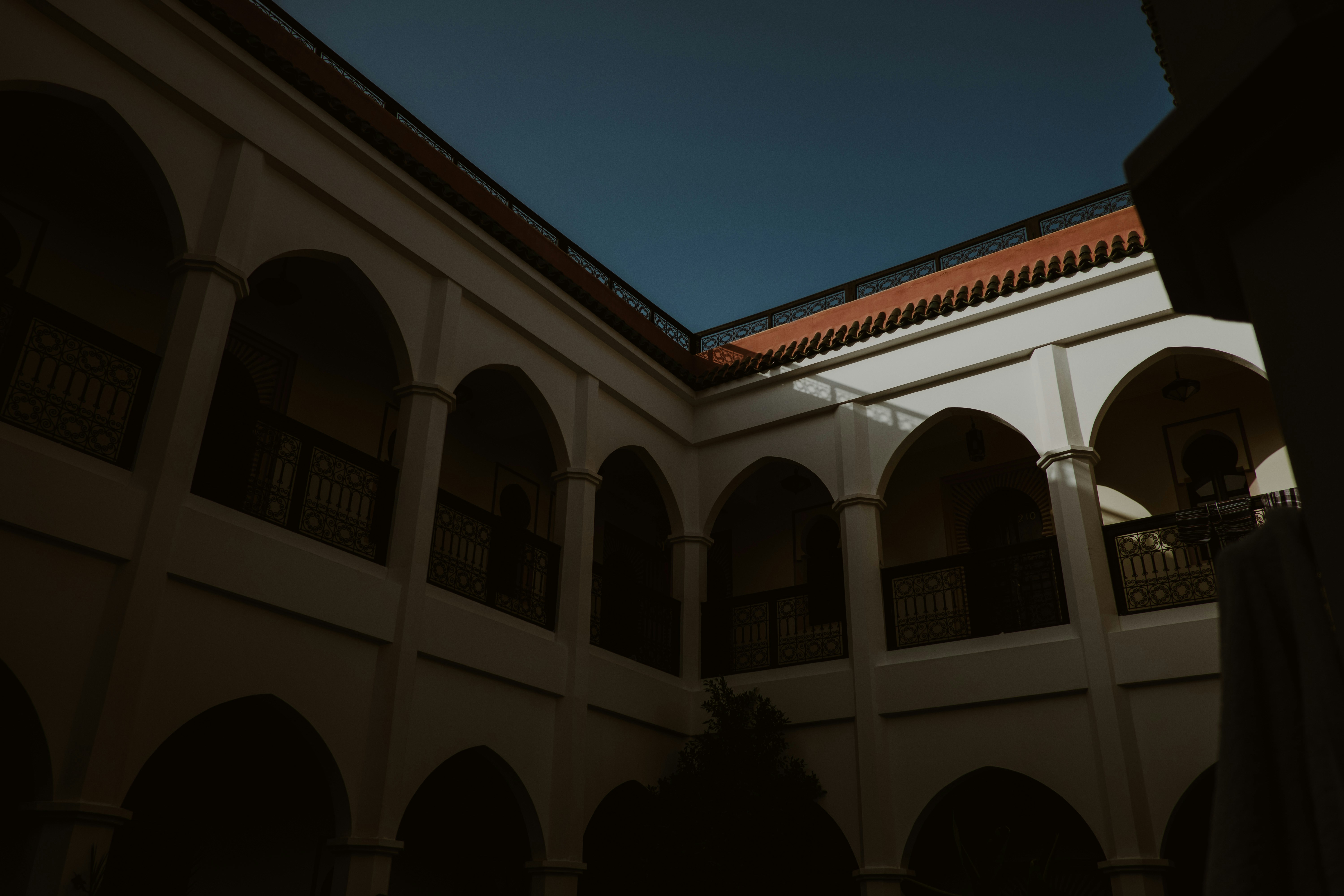 Sunlight filters through a courtyard adorned with arches, casting shadows and highlighting the intricate details of the architecture.