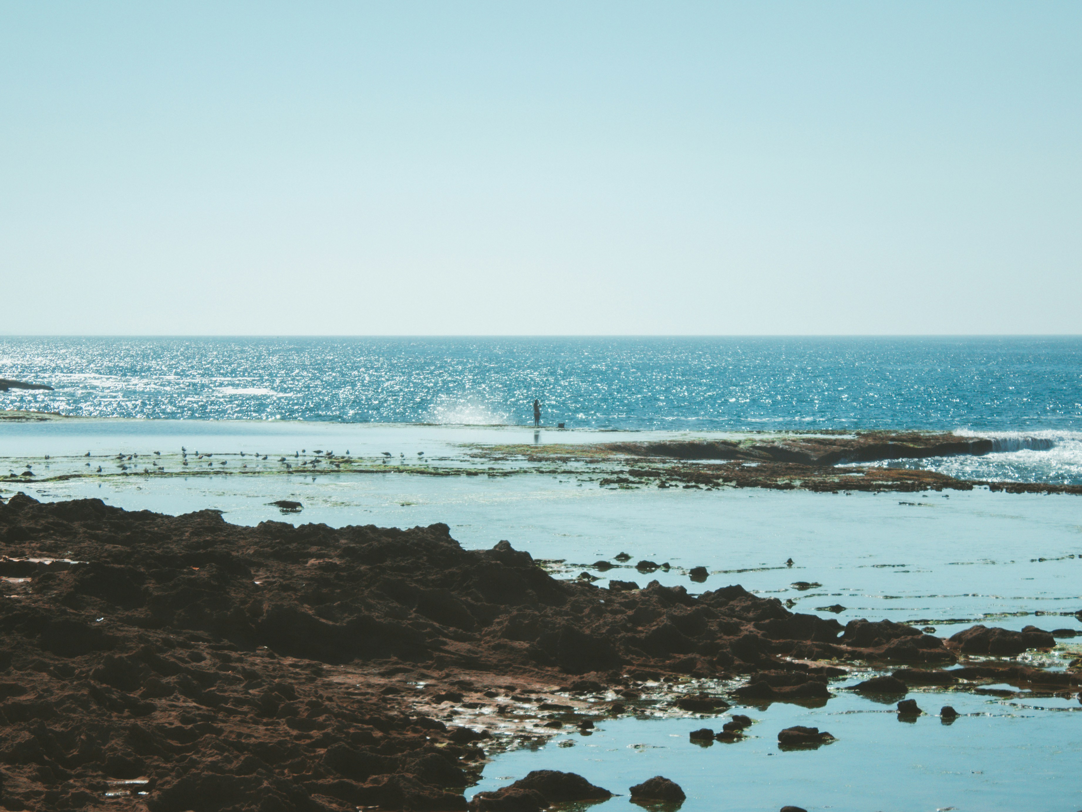 Rocky shoreline with gentle waves meeting the sea under a clear blue sky.