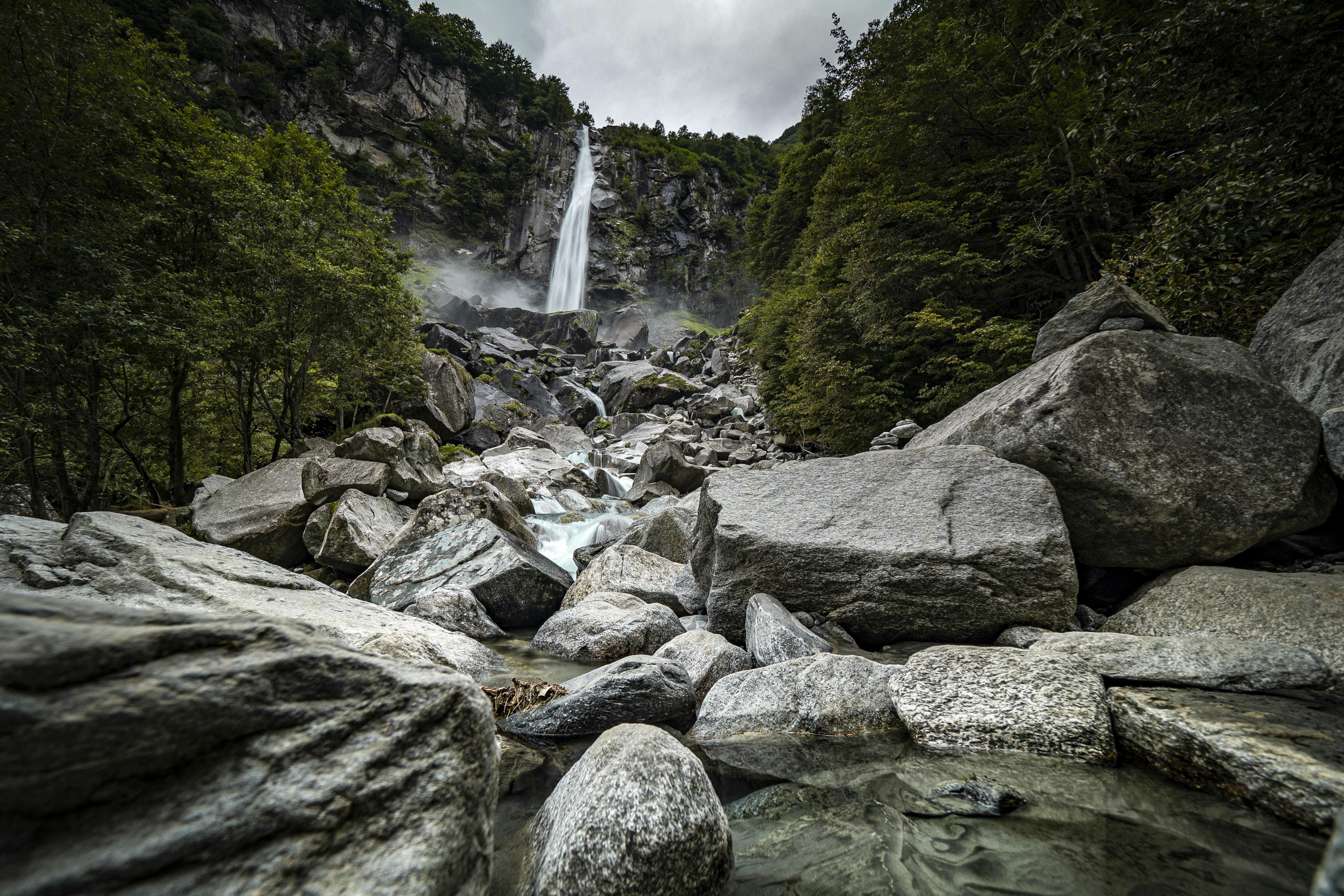 Tall waterfall cascades down rocky cliffs surrounded by lush green forest.