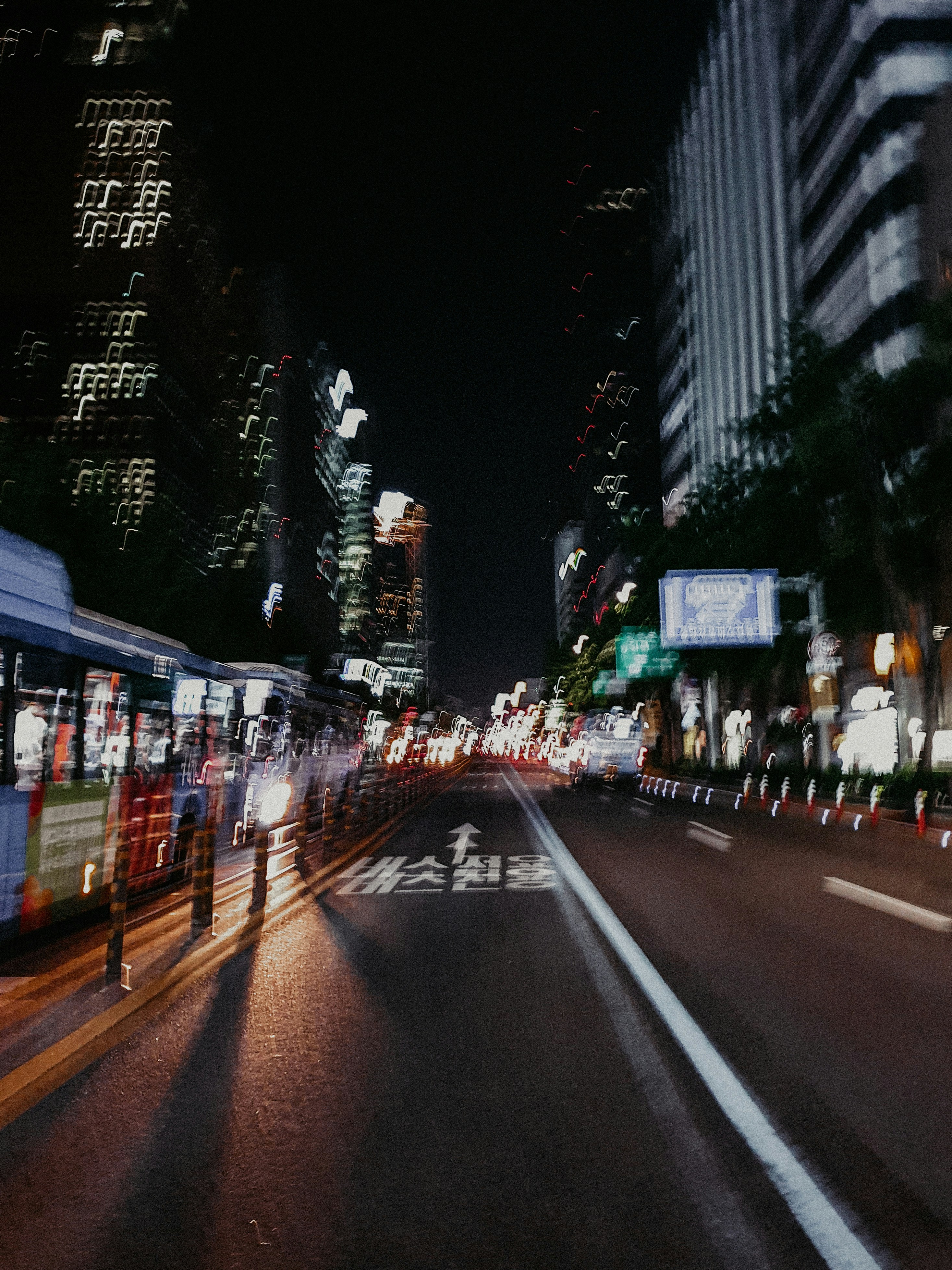 Dynamic view of a bustling city street at night, with blurred lights and tall buildings creating a sense of speed and movement.