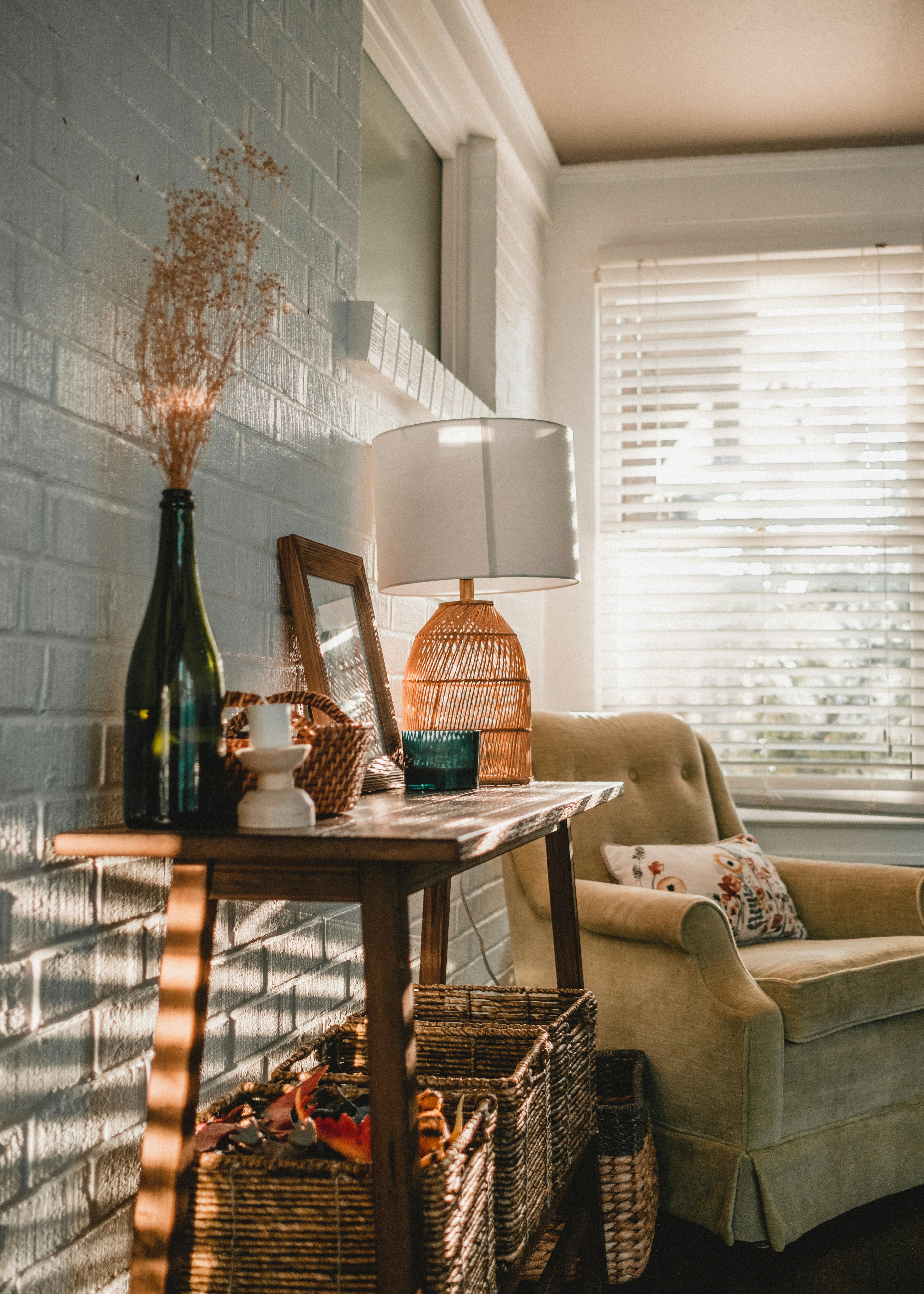 A cozy living space featuring a wooden table adorned with a lamp, decorative items, and a comfortable armchair bathed in soft light.
