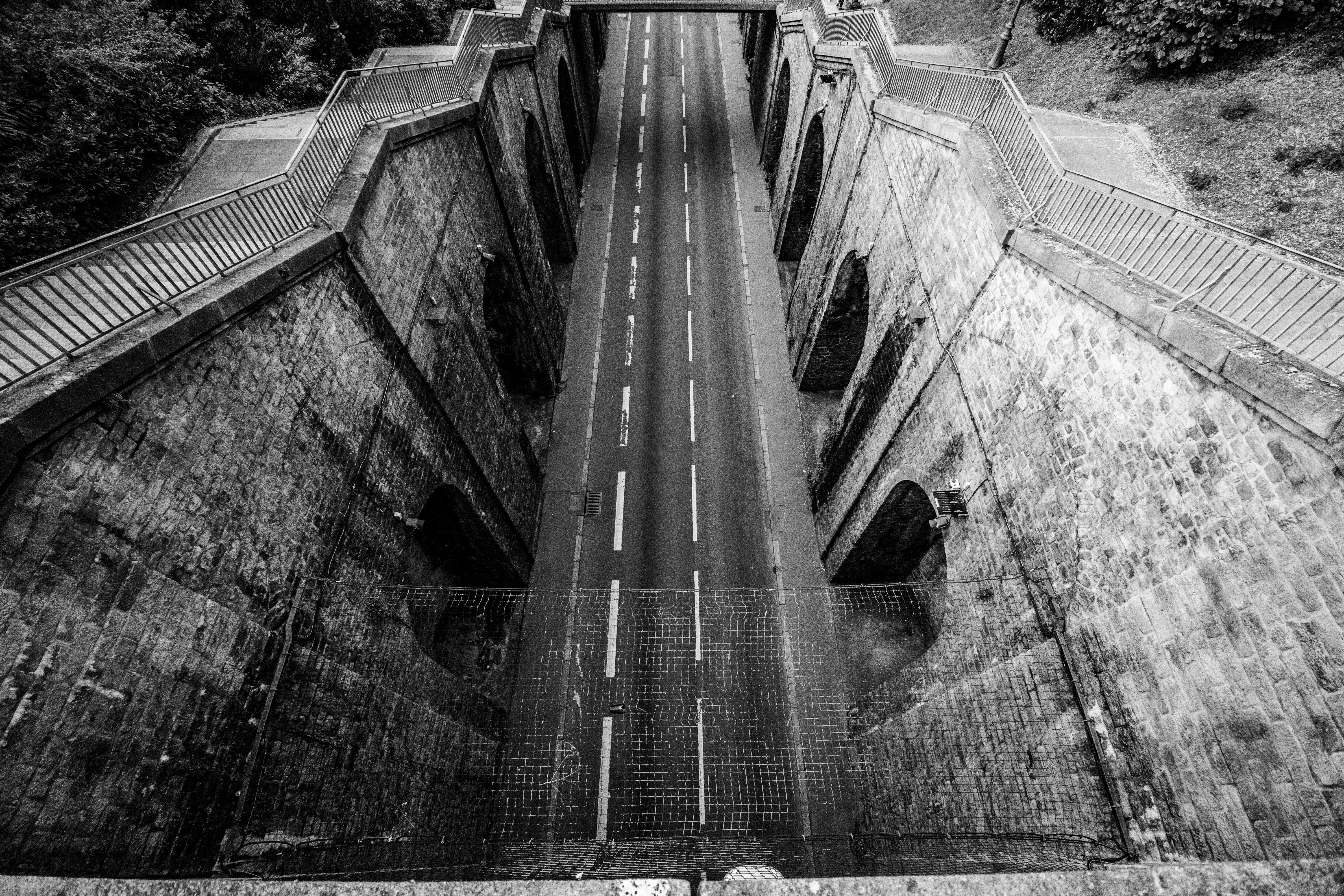 Black and white aerial view of a road passing through a tunnel flanked by stone walls.