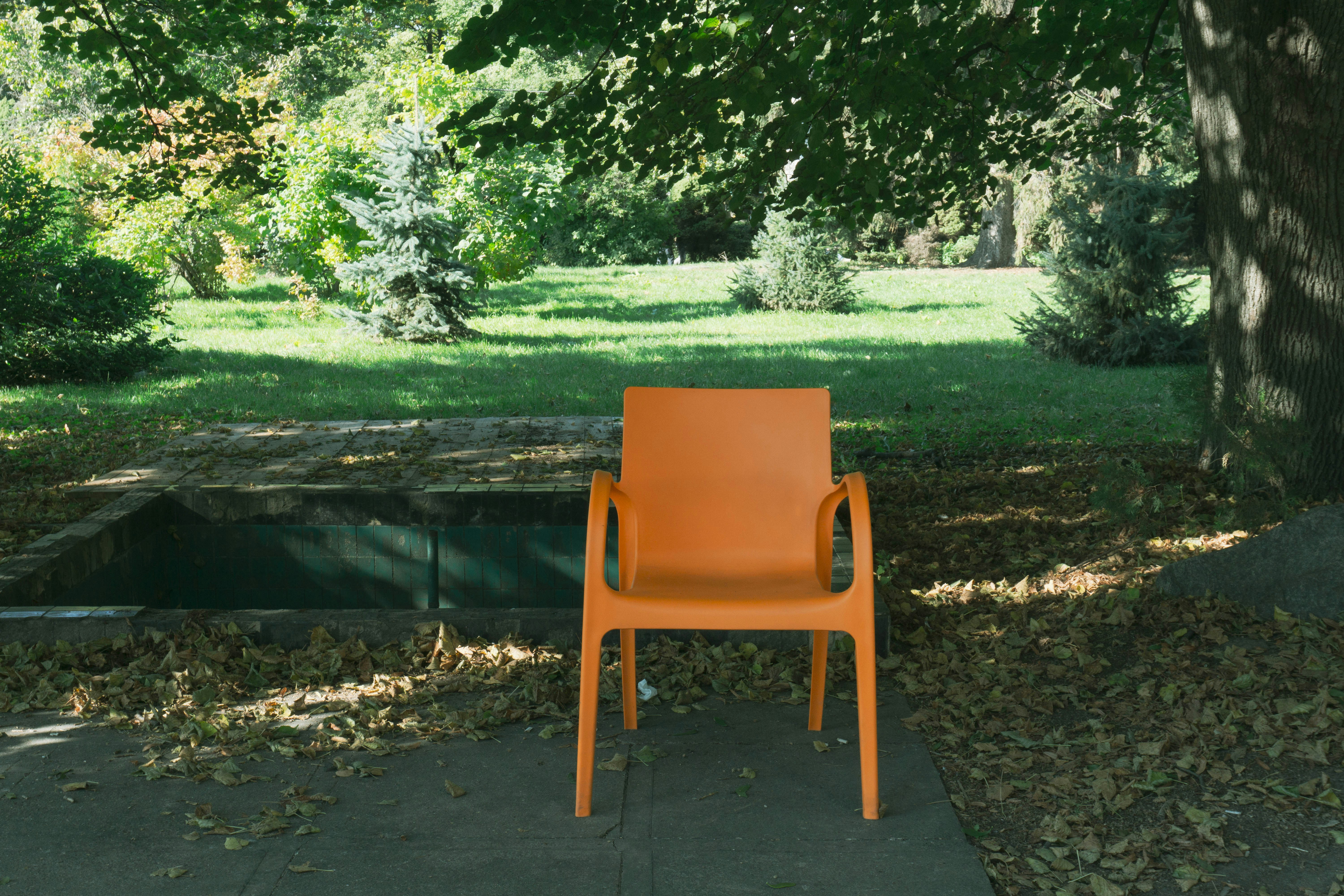 Orange chair on a shaded patio surrounded by lush green trees.