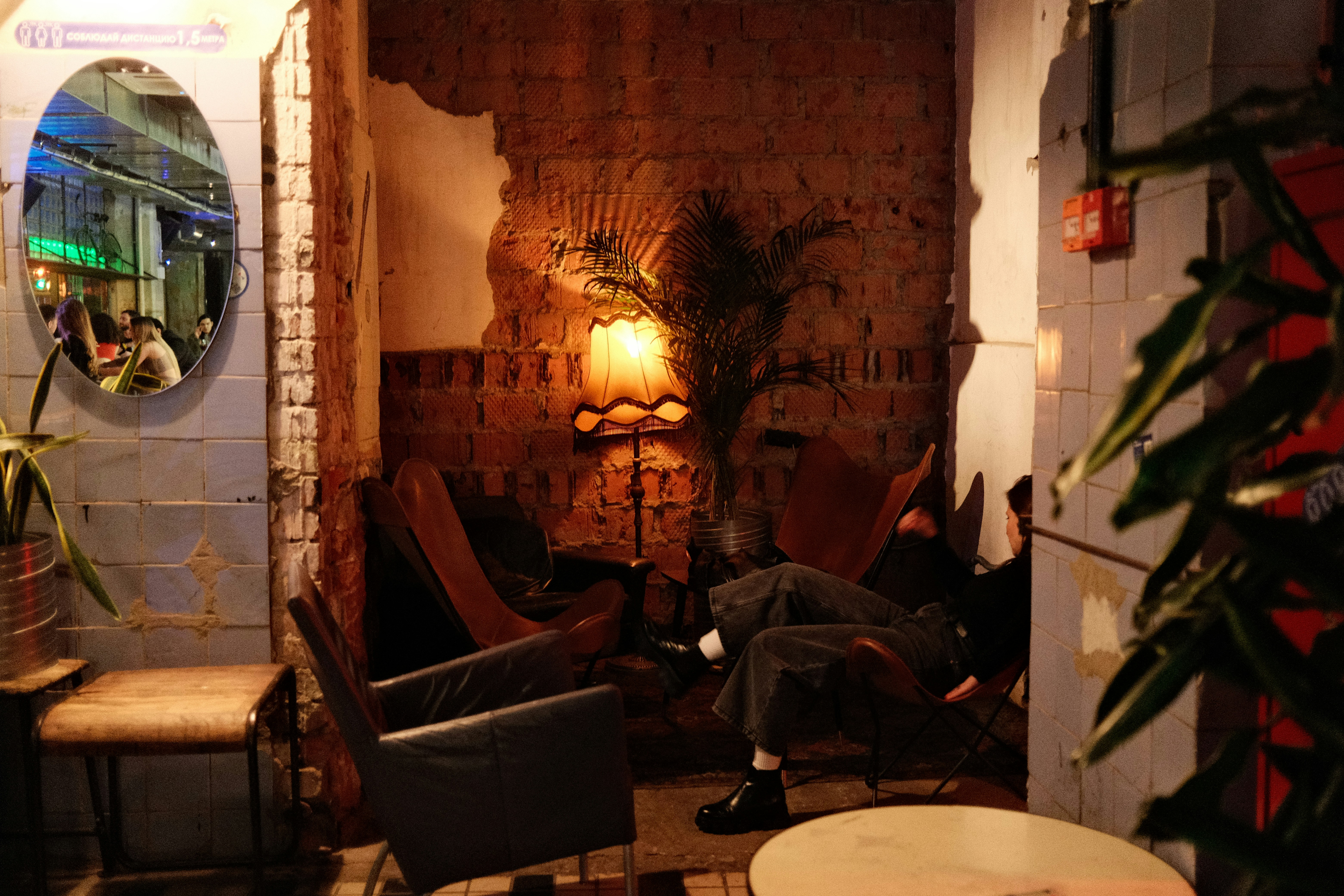 Dimly lit corner of a café featuring vintage chairs, a glowing lamp, and a mirror reflecting the ambiance.