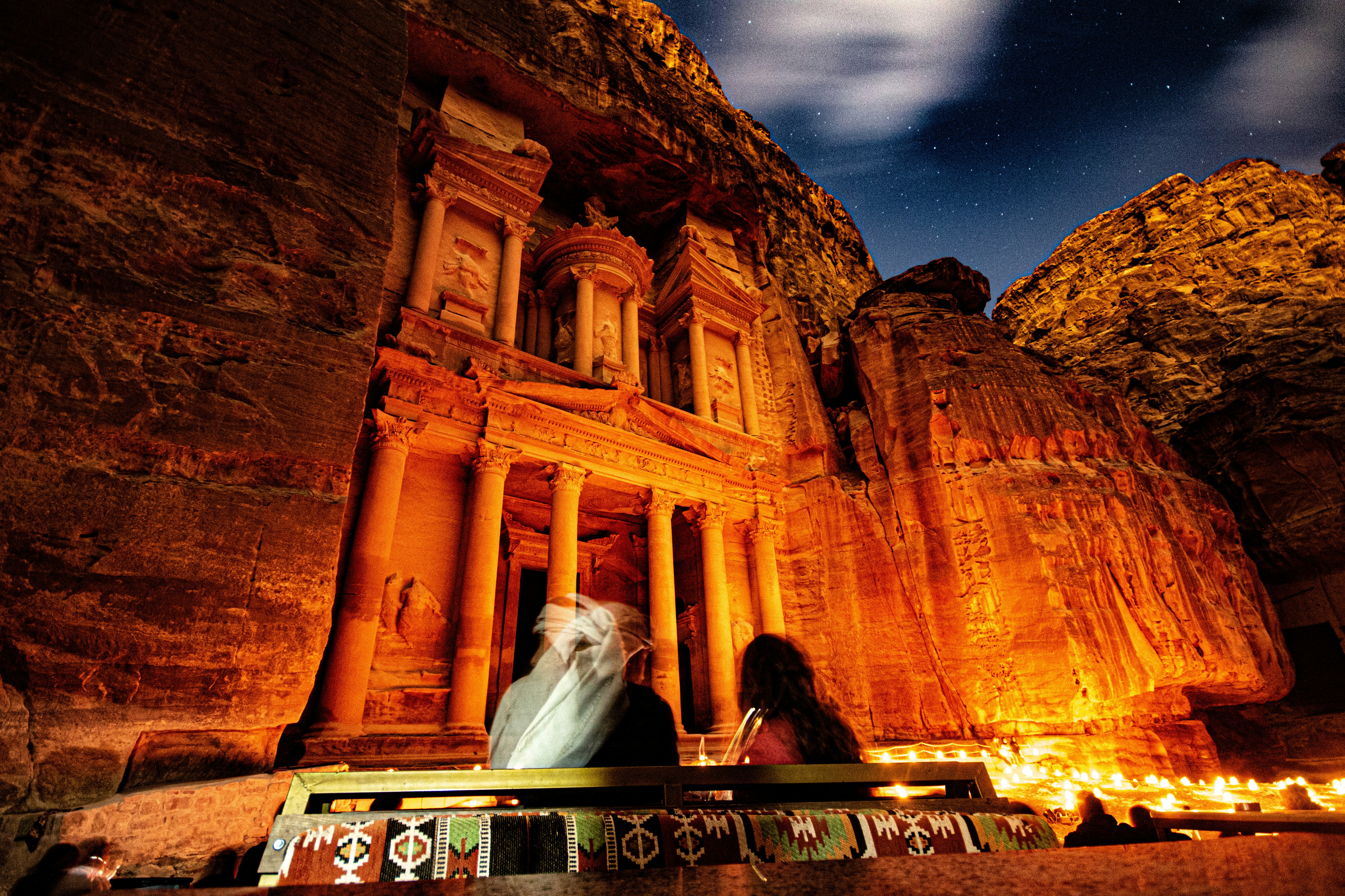 The illuminated facade of Petra's Treasury under a starry night sky.