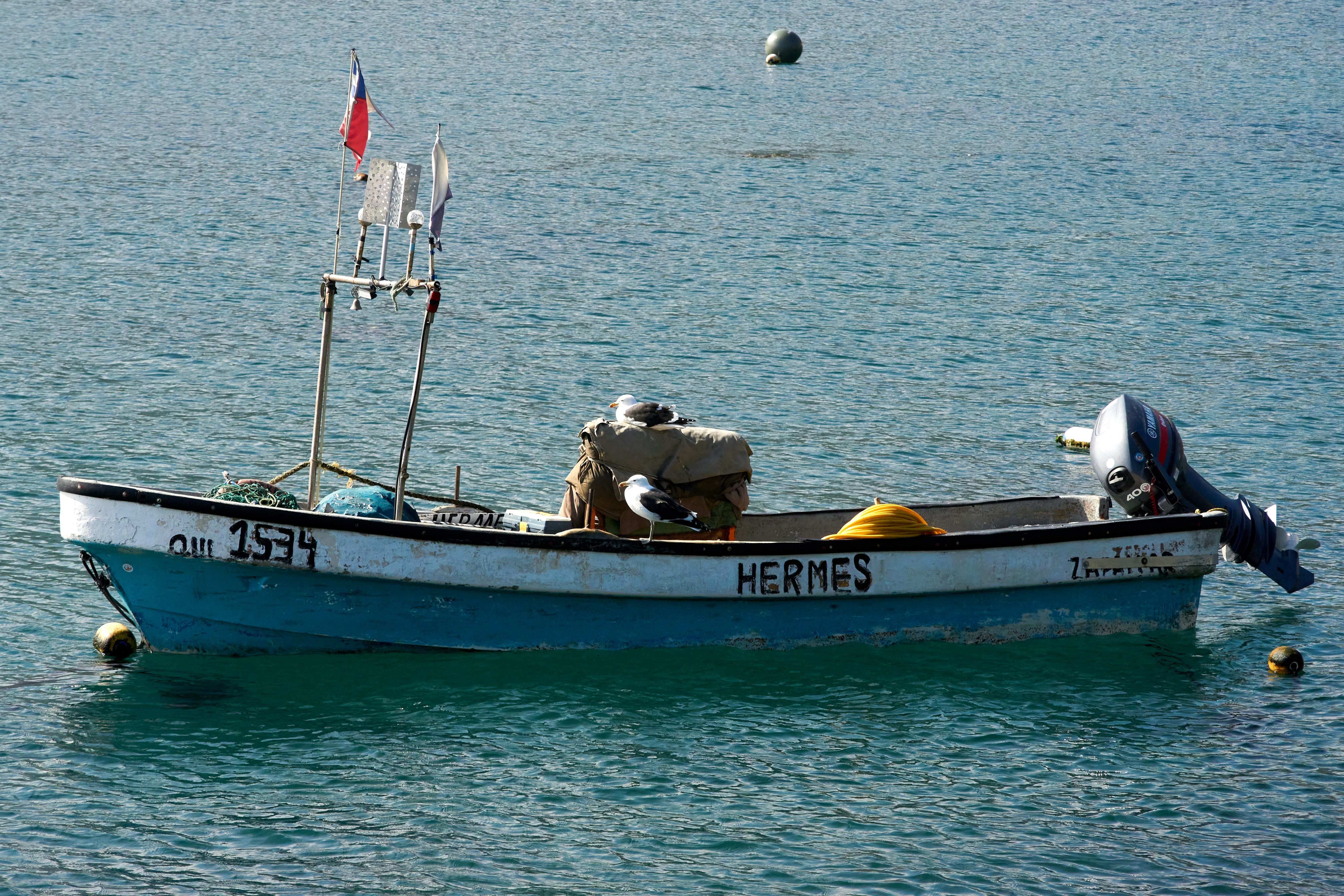 A small fishing boat named 'HERMES' anchored in calm turquoise waters, adorned with flags and fishing gear.