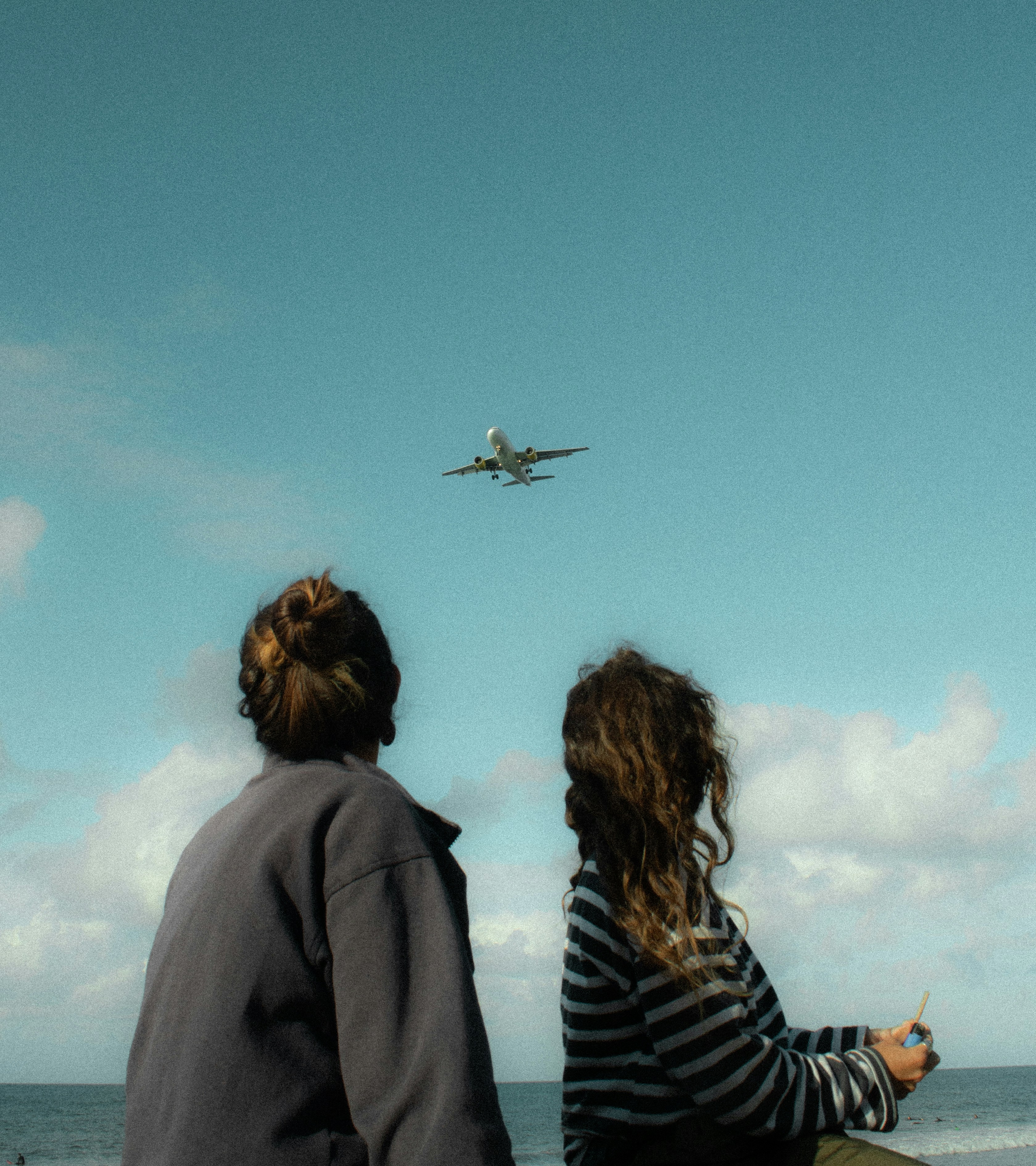 Two people looking at an airplane flying over the ocean photo – Free ...