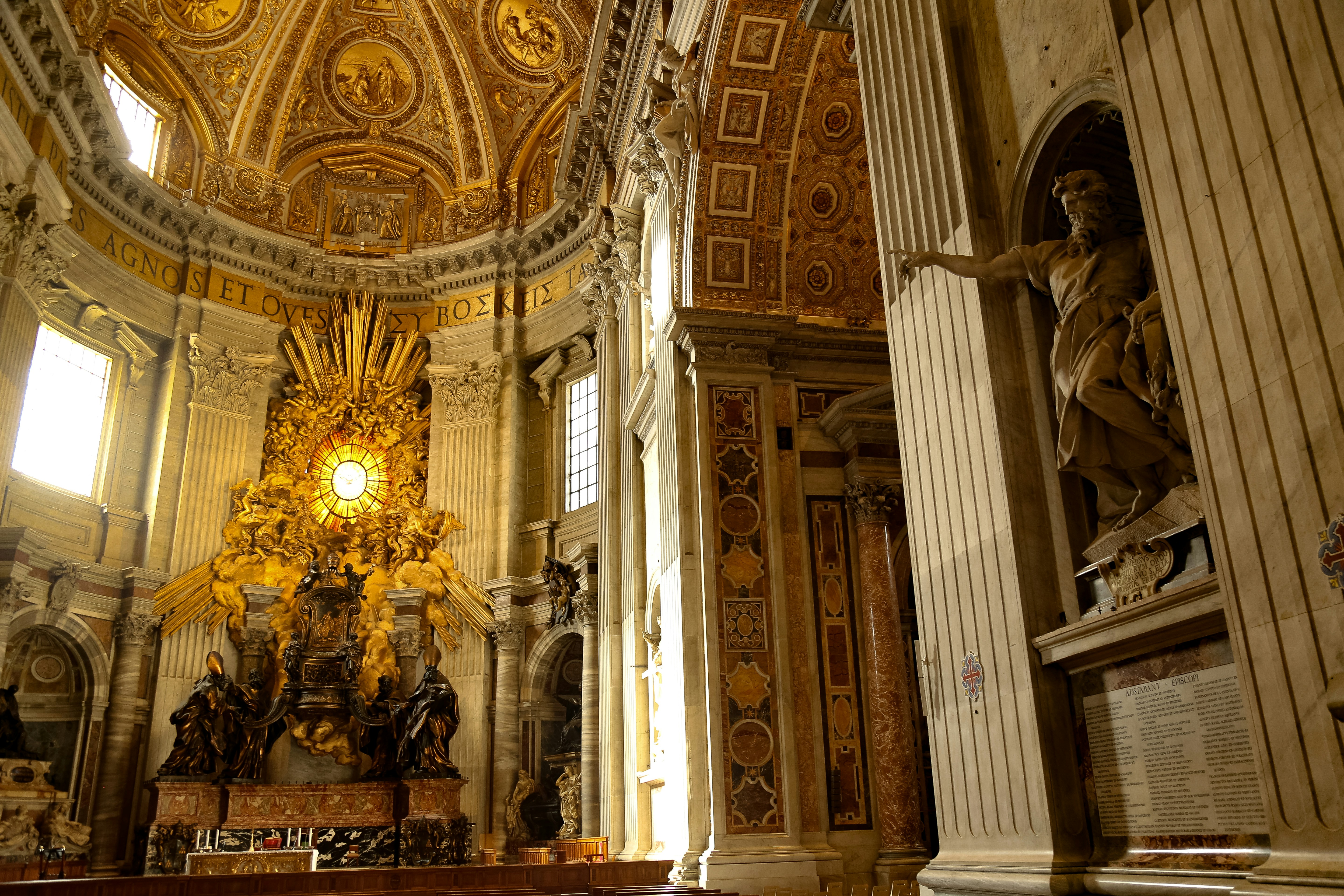 Ornate interior of a grand basilica showcasing a dramatic altar and a striking statue, illuminated by natural light filtering through large windows.