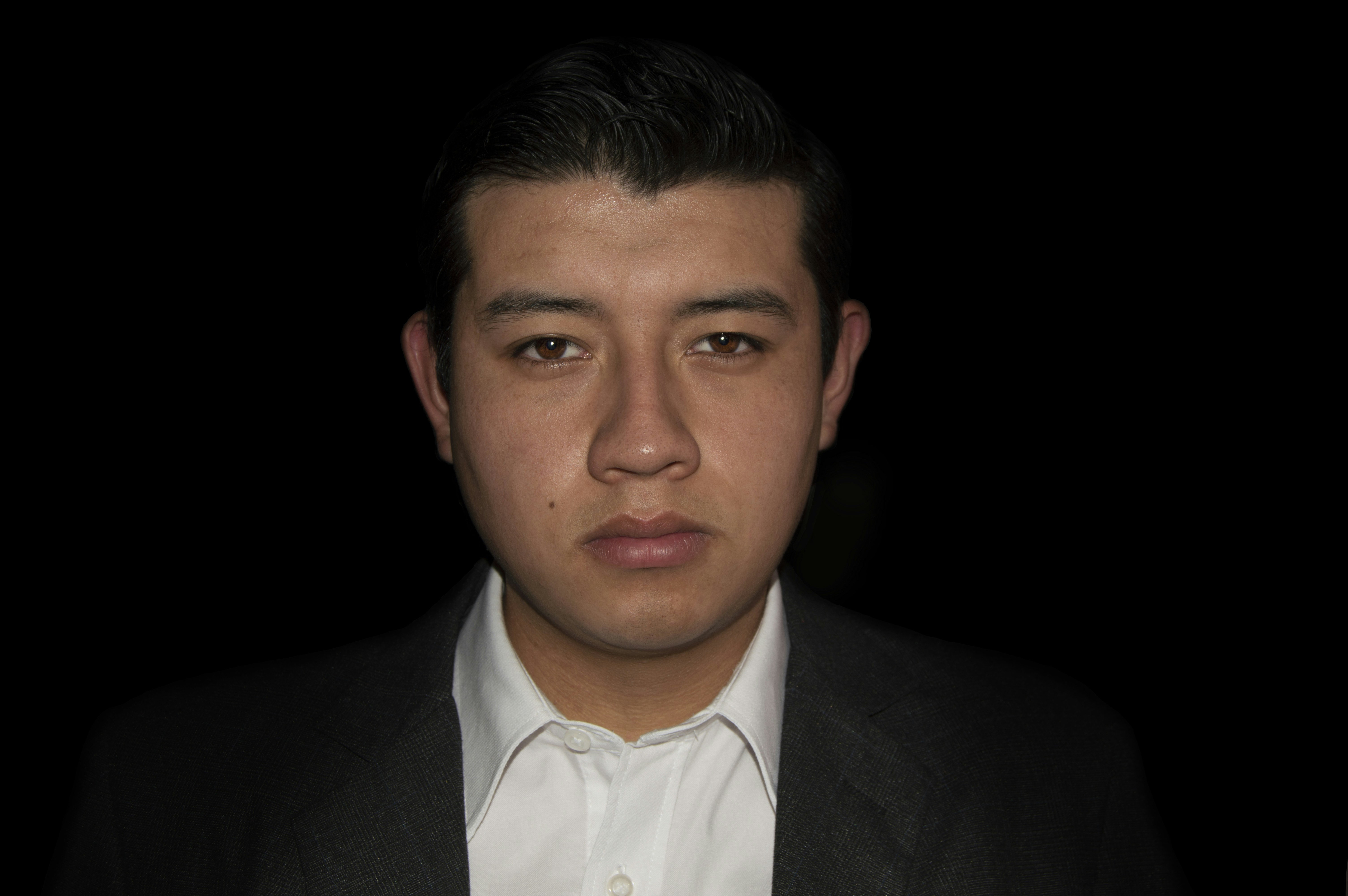 Man in a suit and tie with a serious expression against a dark background.