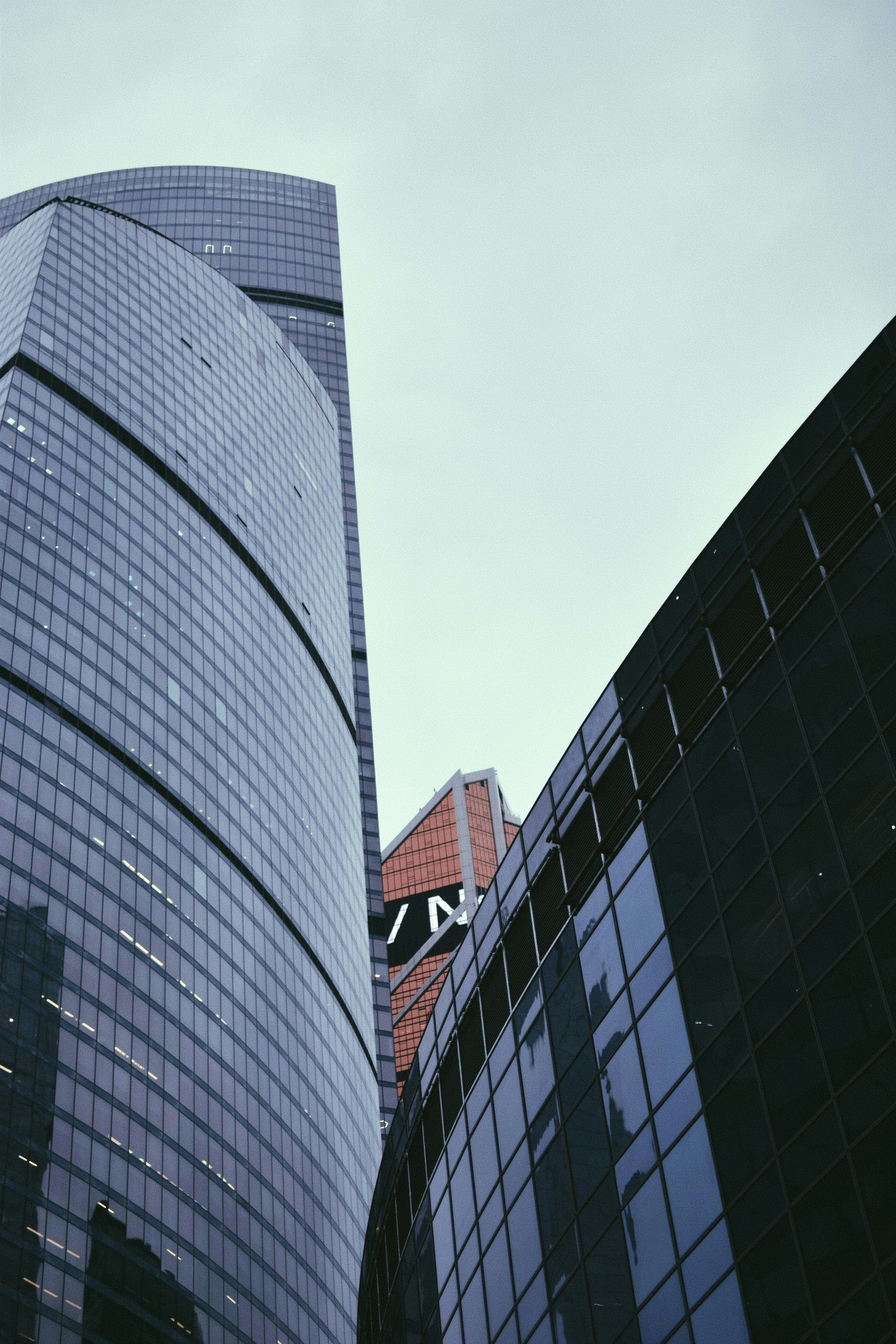 Two modern skyscrapers converge in a dynamic architectural composition, showcasing their sleek glass facades against a muted sky.