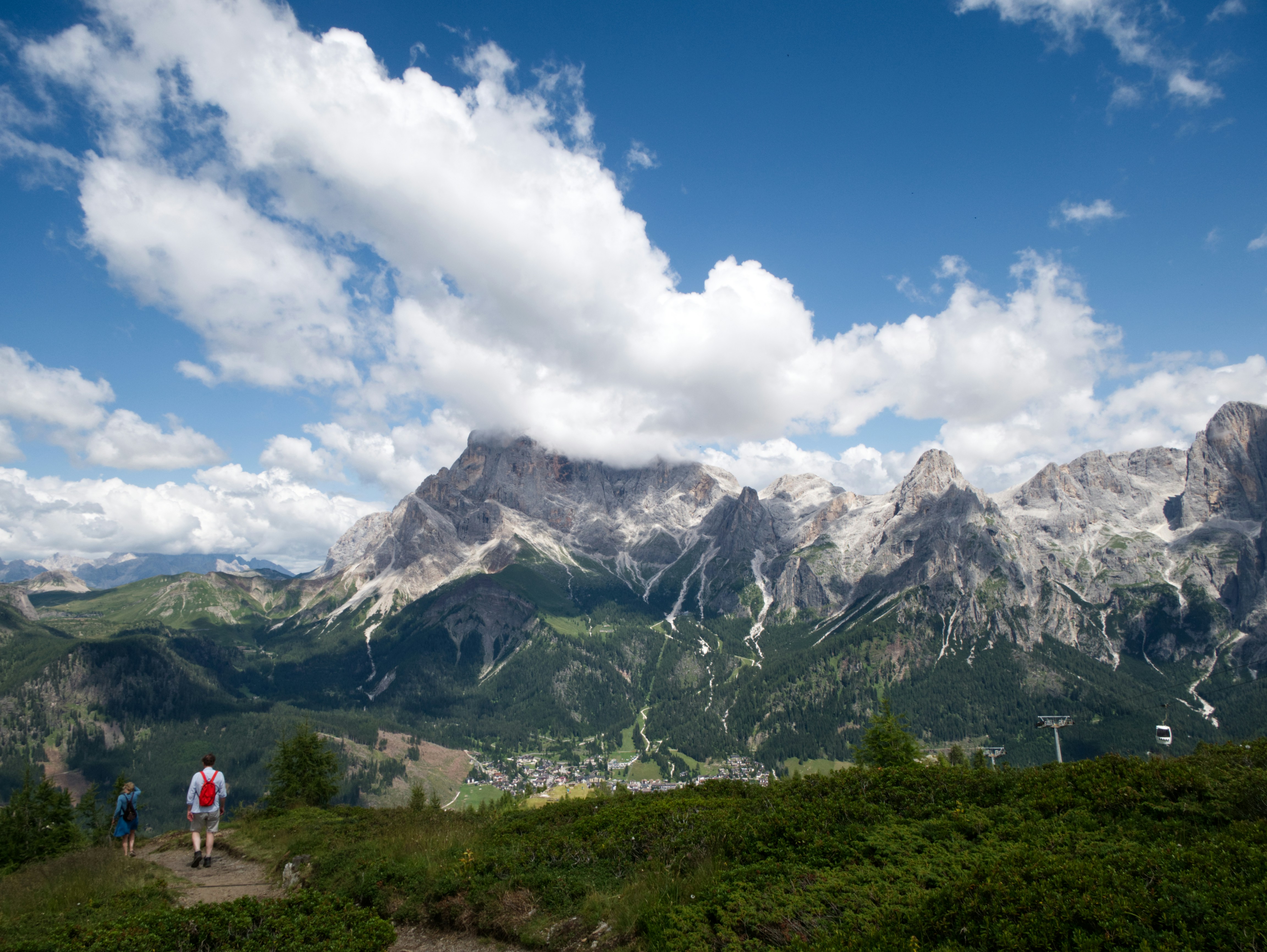 Two hikers traverse a scenic mountain trail, surrounded by the towering peaks of the Dolomites under a vibrant sky.