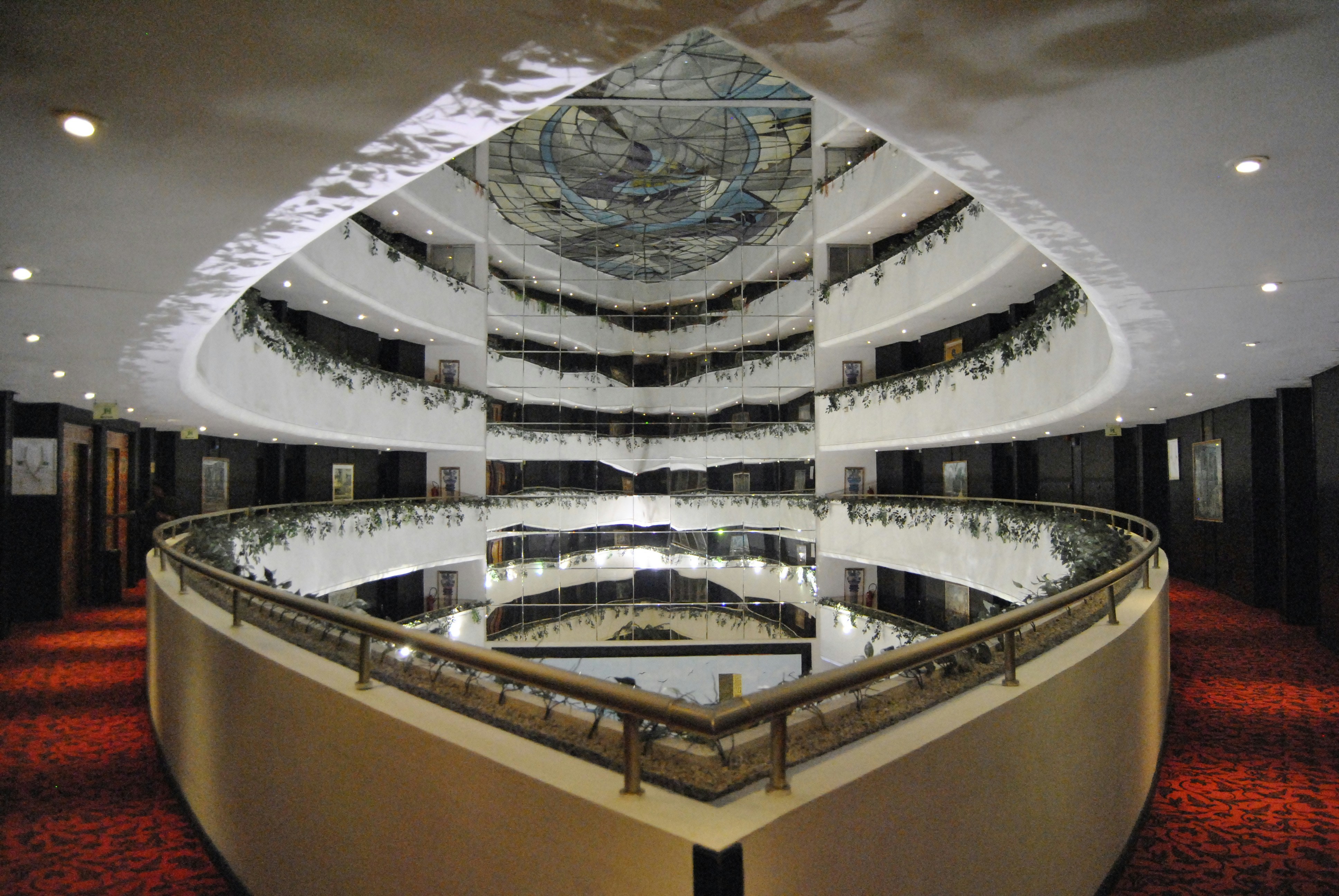 Interior view of a modern atrium showcasing a spiral design with lush greenery and artistic ceiling details.
