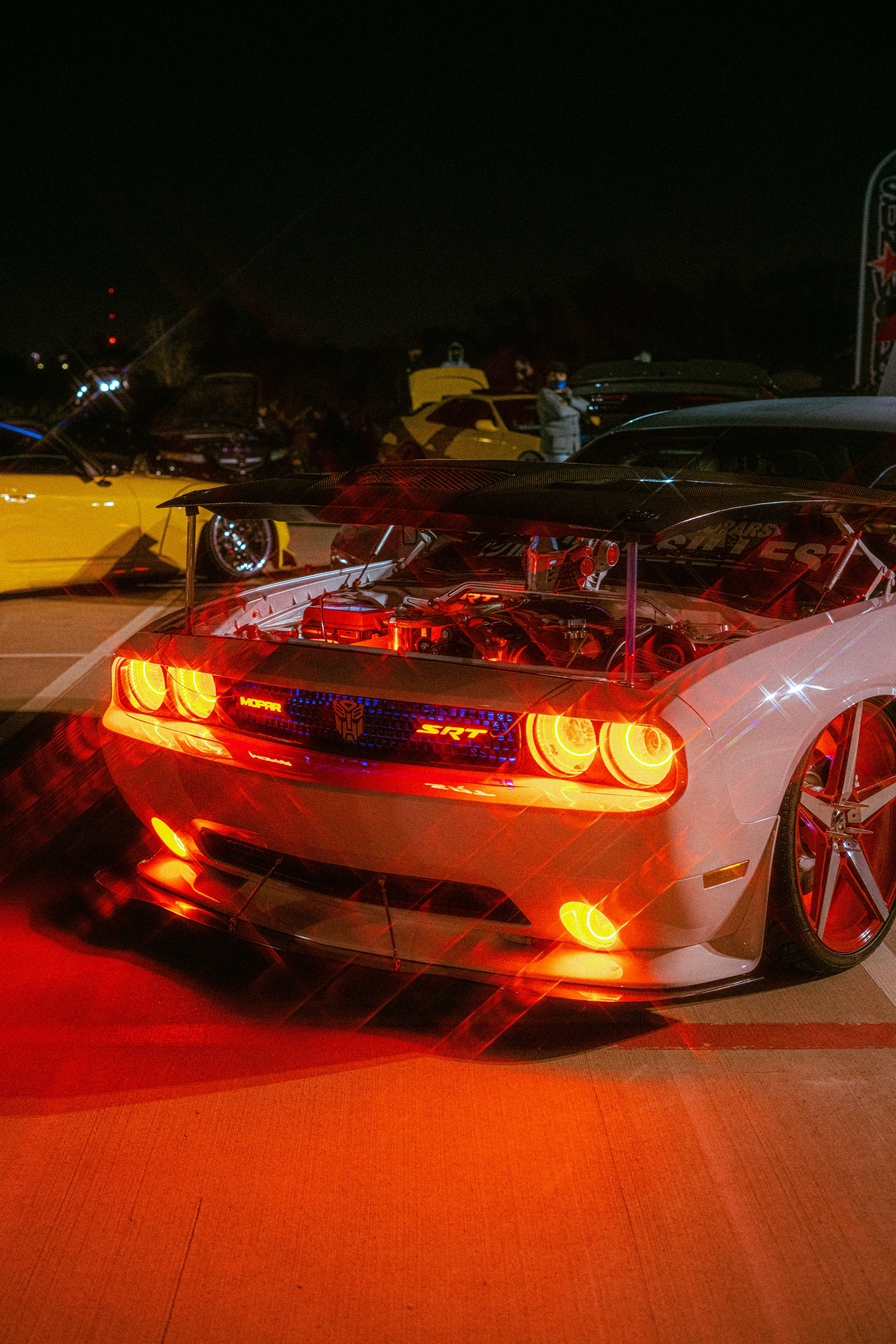 Modified white muscle car with an open hood showcasing a vibrant engine illuminated by red lights.