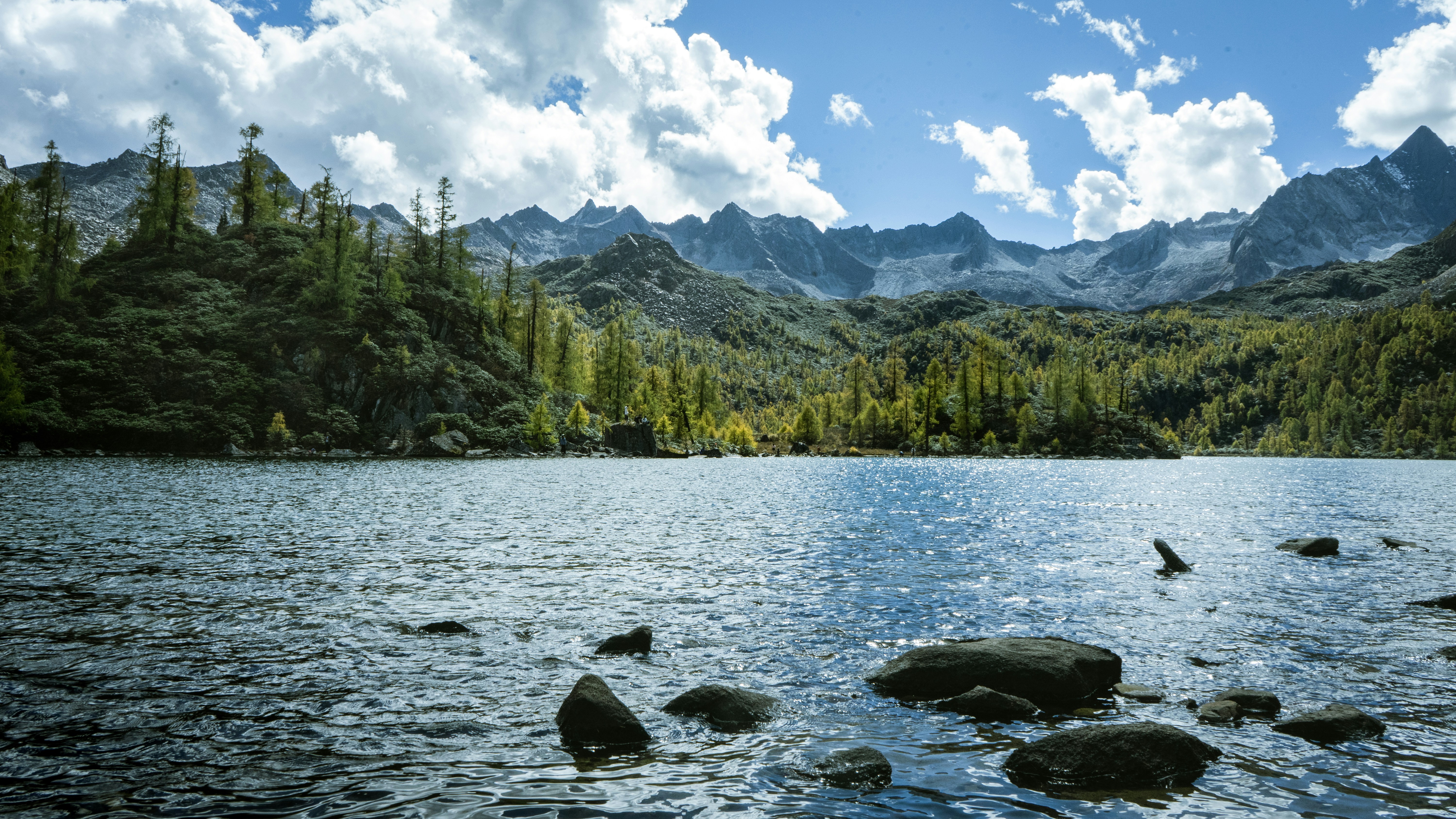 Tranquil mountain lake surrounded by lush greenery and rugged peaks under a partly cloudy sky.