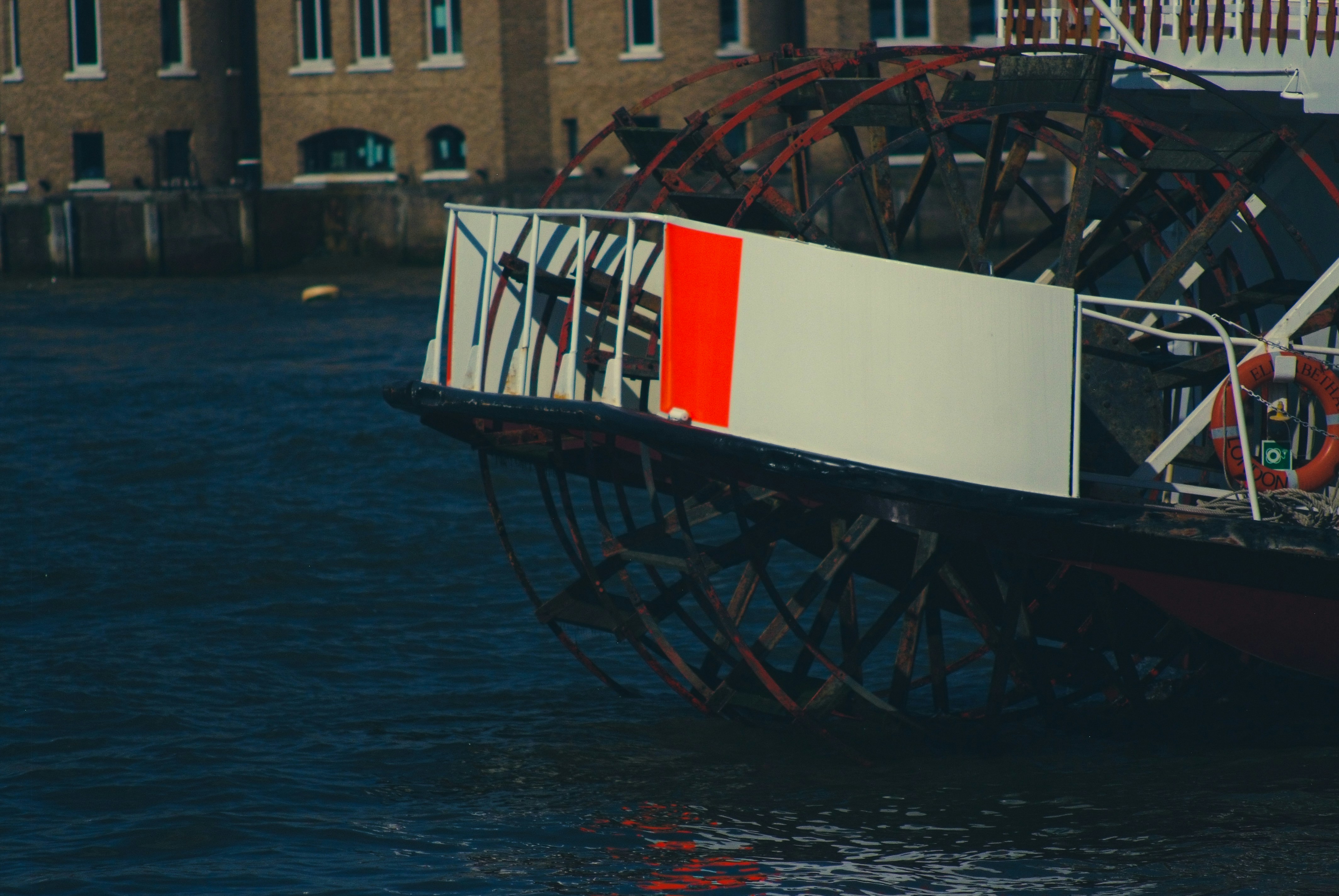 Paddlewheel boat partially submerged in the river, showcasing its intricate wheel structure against a backdrop of brick buildings.