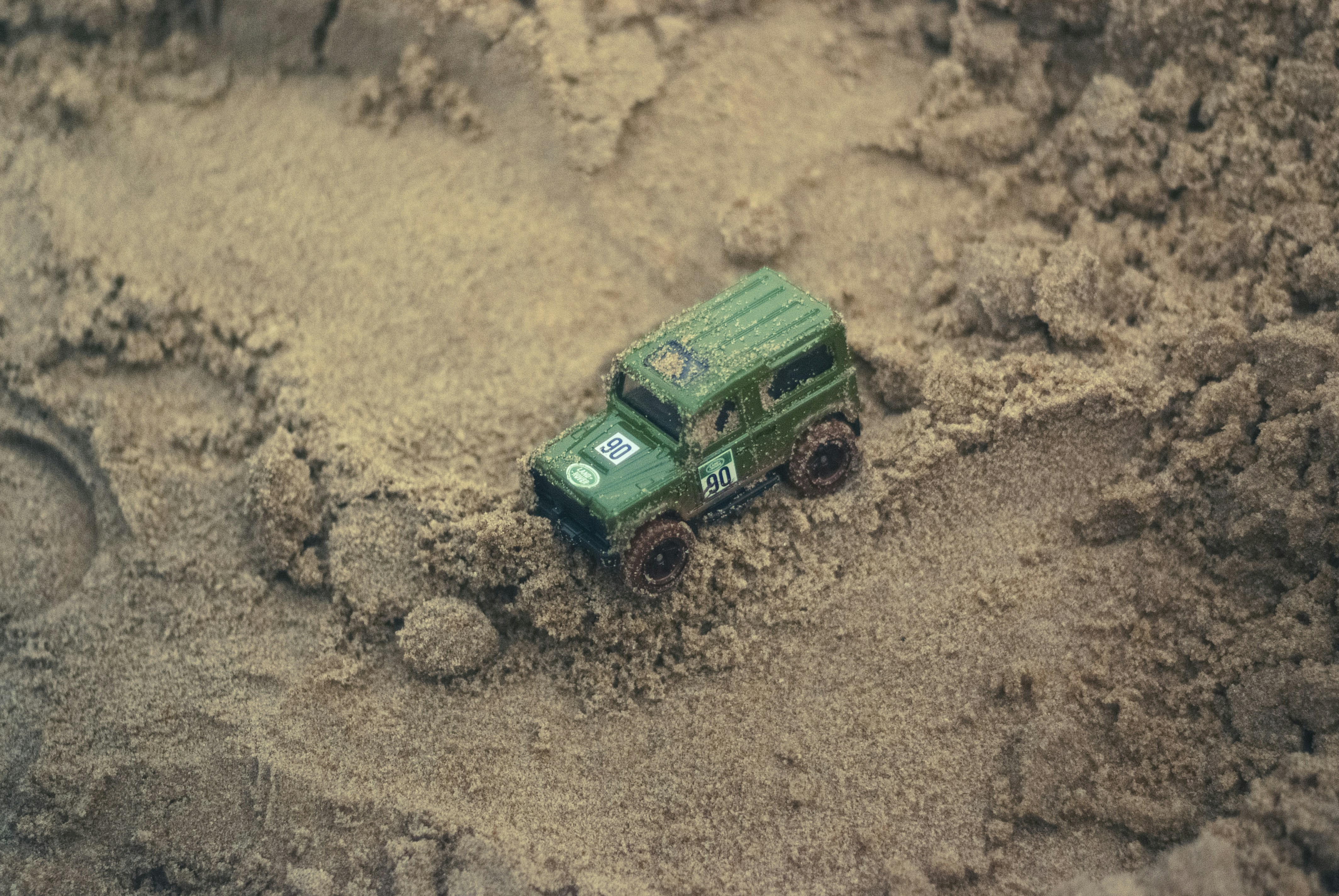 A green toy jeep navigating through a sandy landscape, showcasing its rugged design against the textured backdrop of sand.