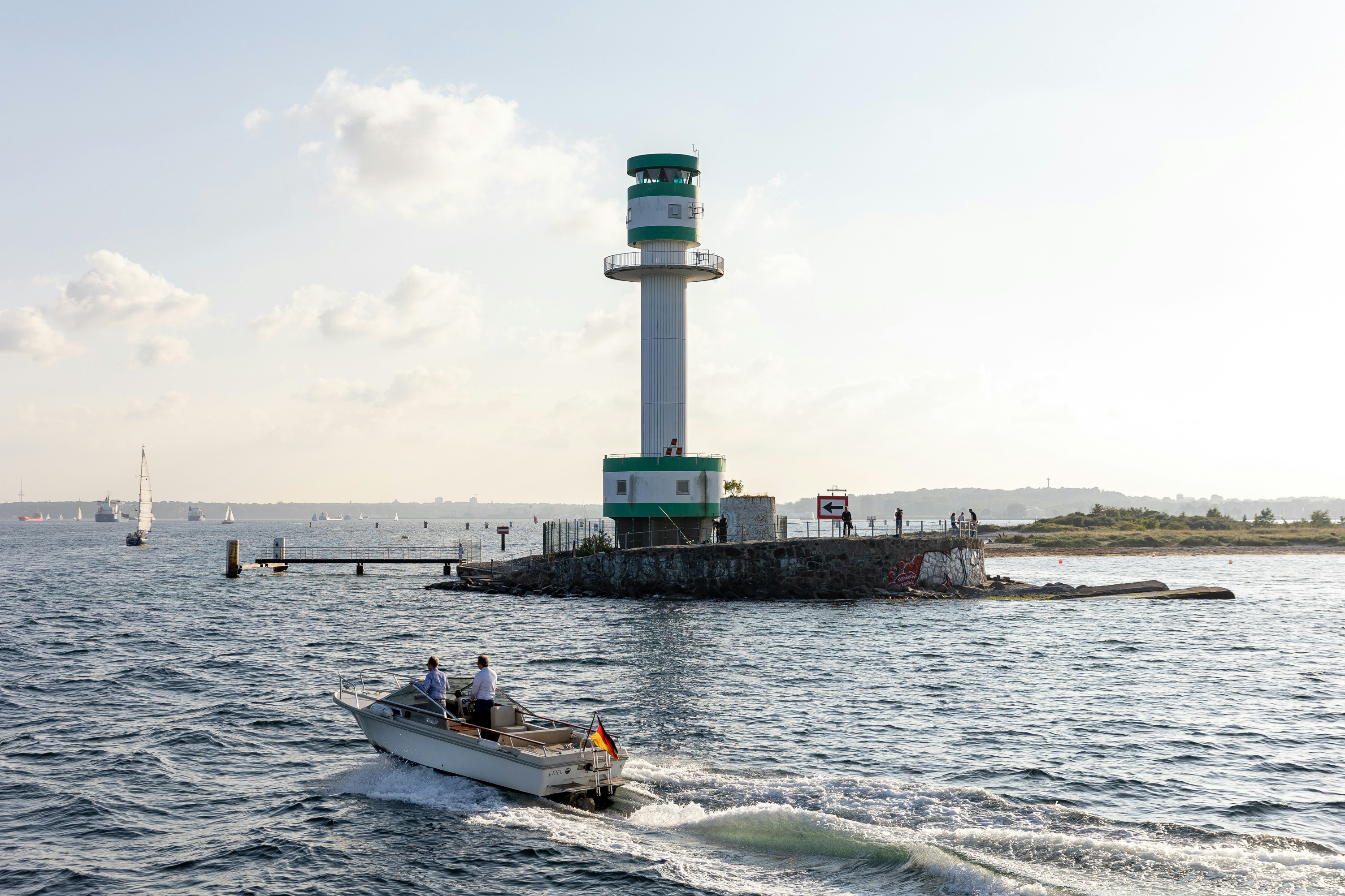 Small boat cruising near a modern lighthouse under a partly cloudy sky.