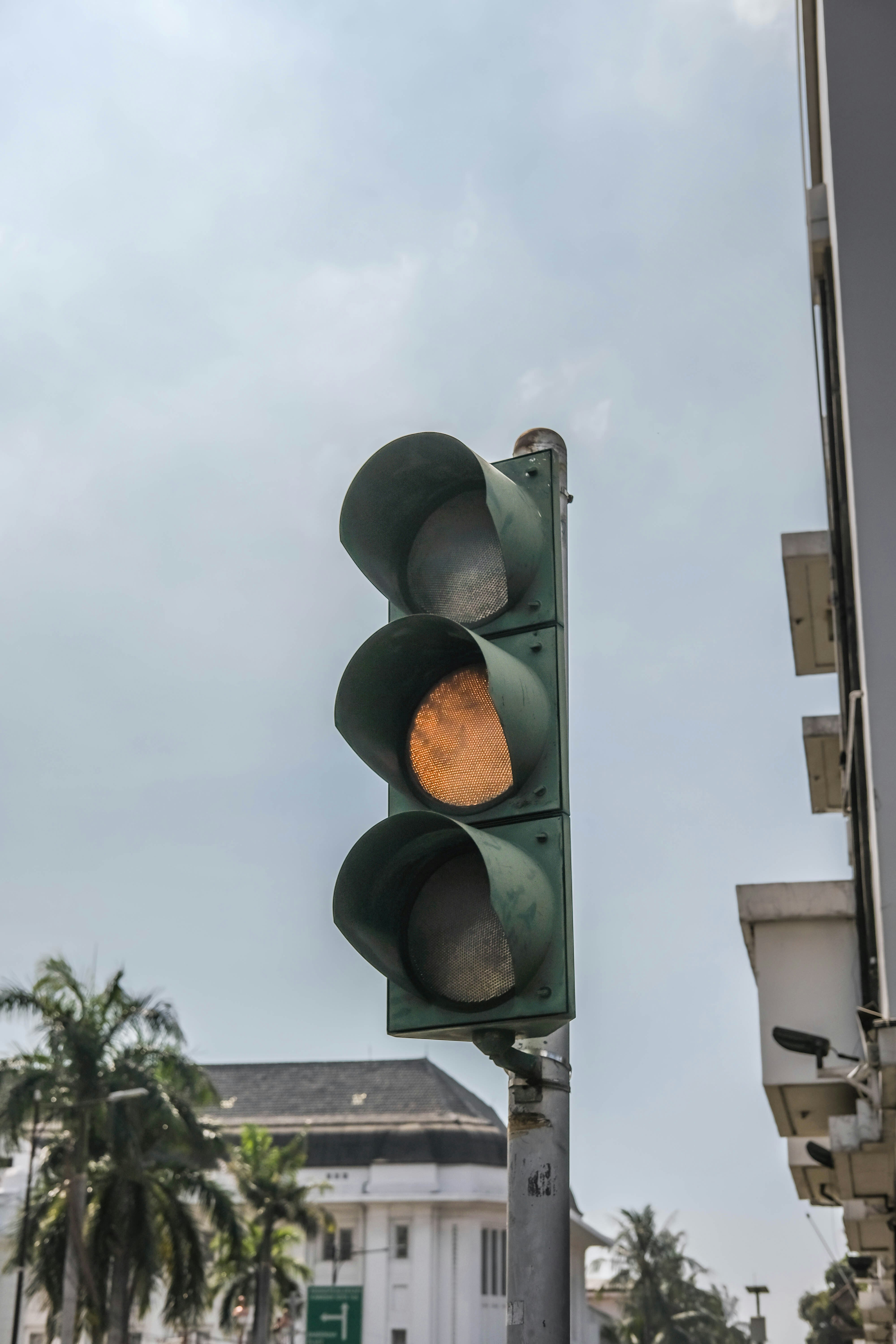 Traffic light displaying yellow signal against a cloudy sky, with surrounding urban architecture visible. 