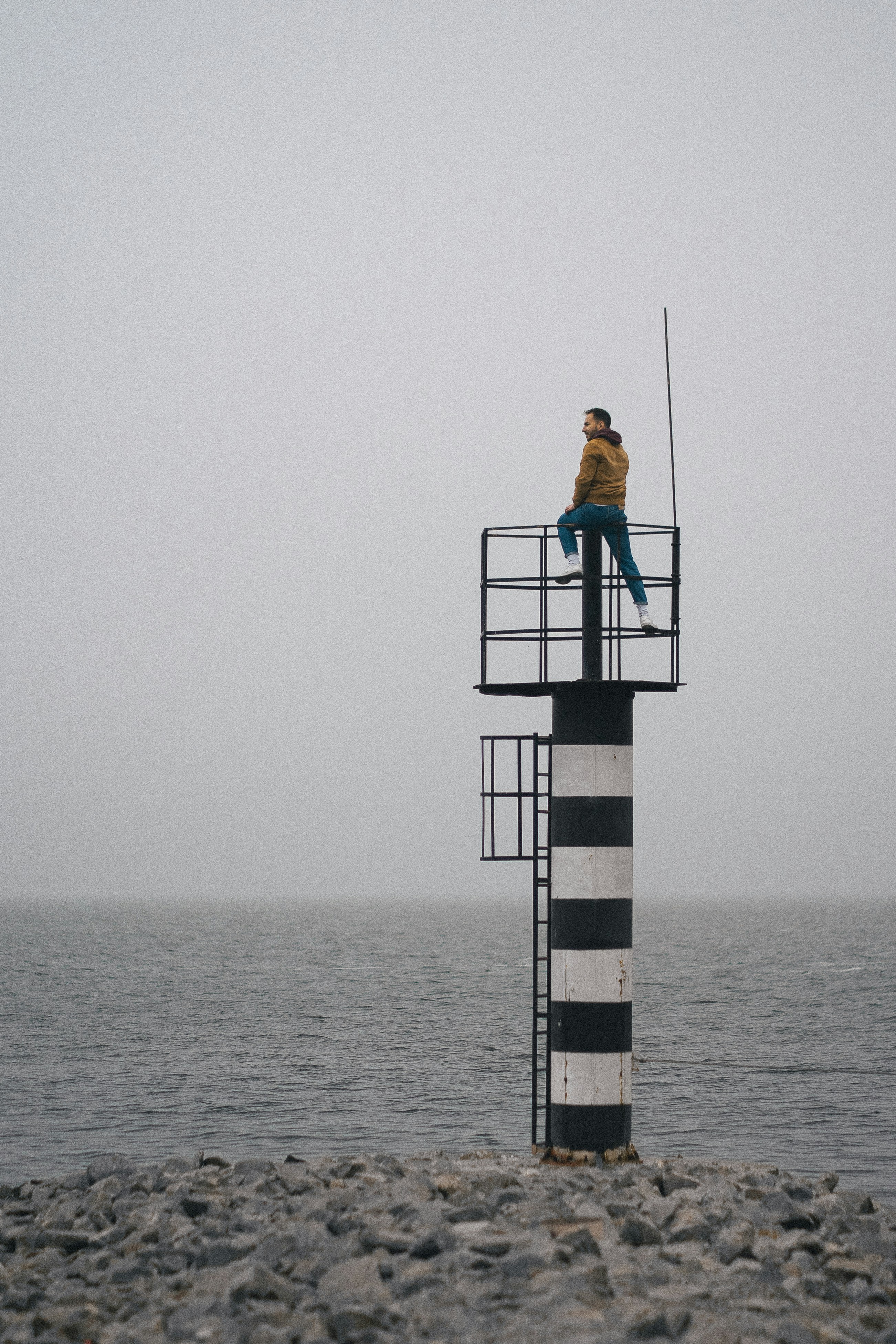 Lone Observer on a Striped Beacon Over the Quiet Sea