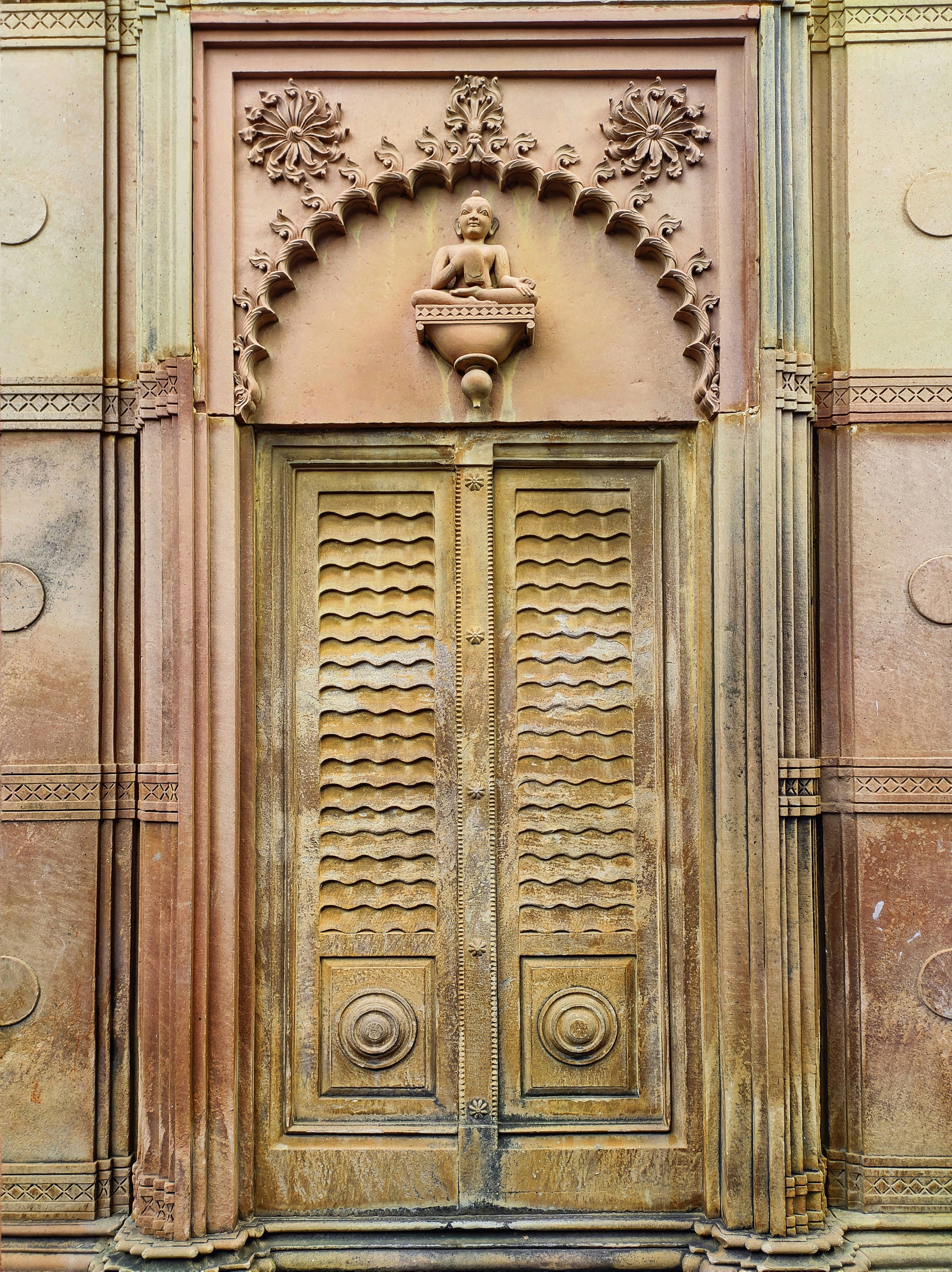 Ornately carved door featuring a statue above, showcasing traditional craftsmanship and architectural detail.