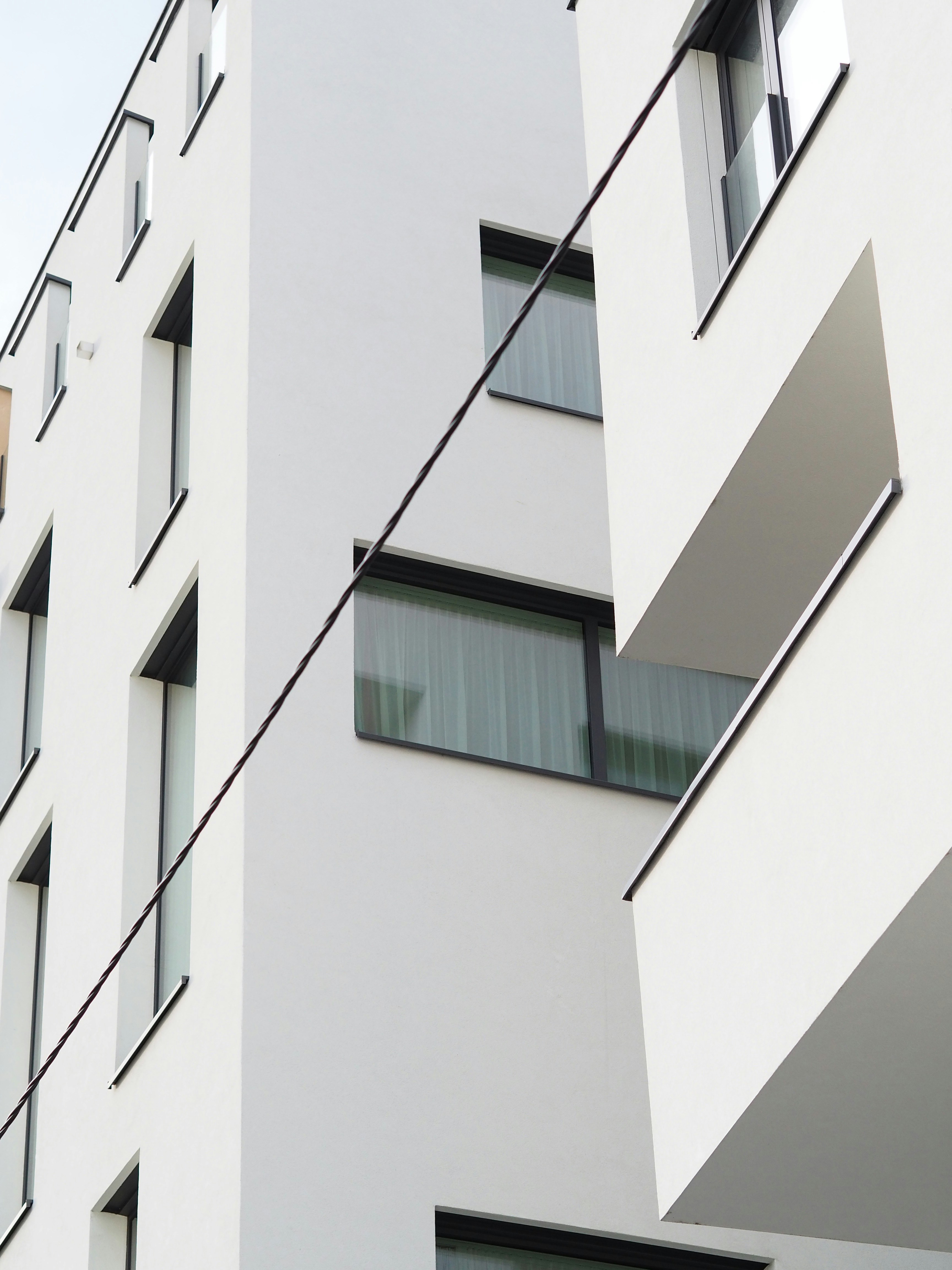 Modern apartment building showcasing a minimalist design with clean lines and large windows. The composition emphasizes the interplay of light and shadow.