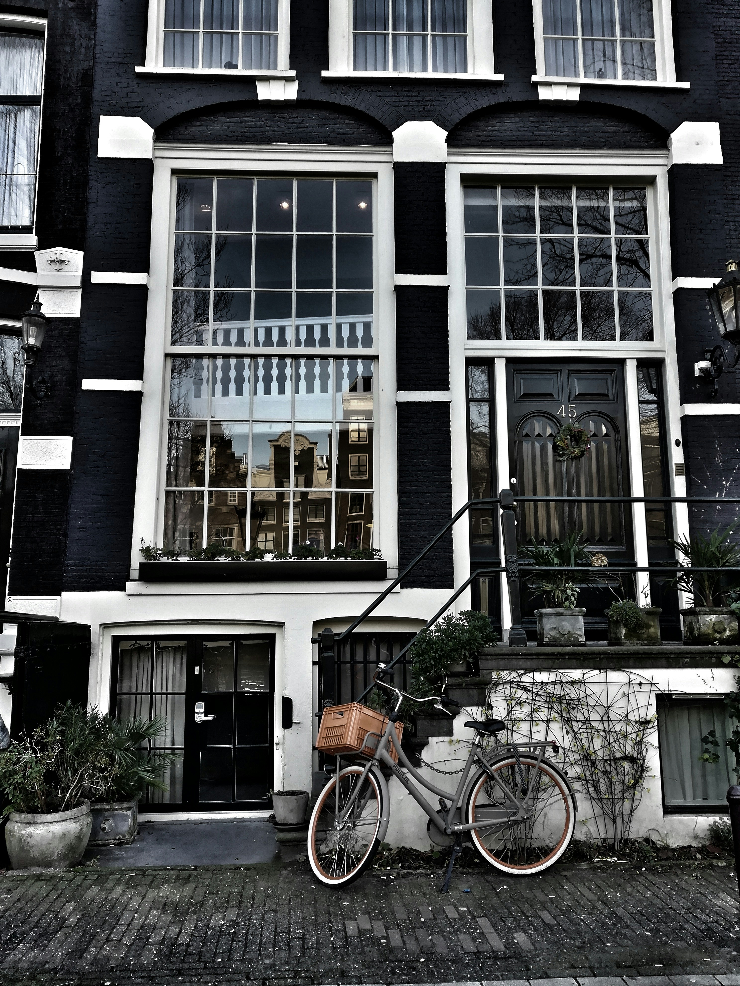 Charming Amsterdam facade featuring large windows, a wooden door, and a parked bicycle, reflecting the city's architectural elegance.