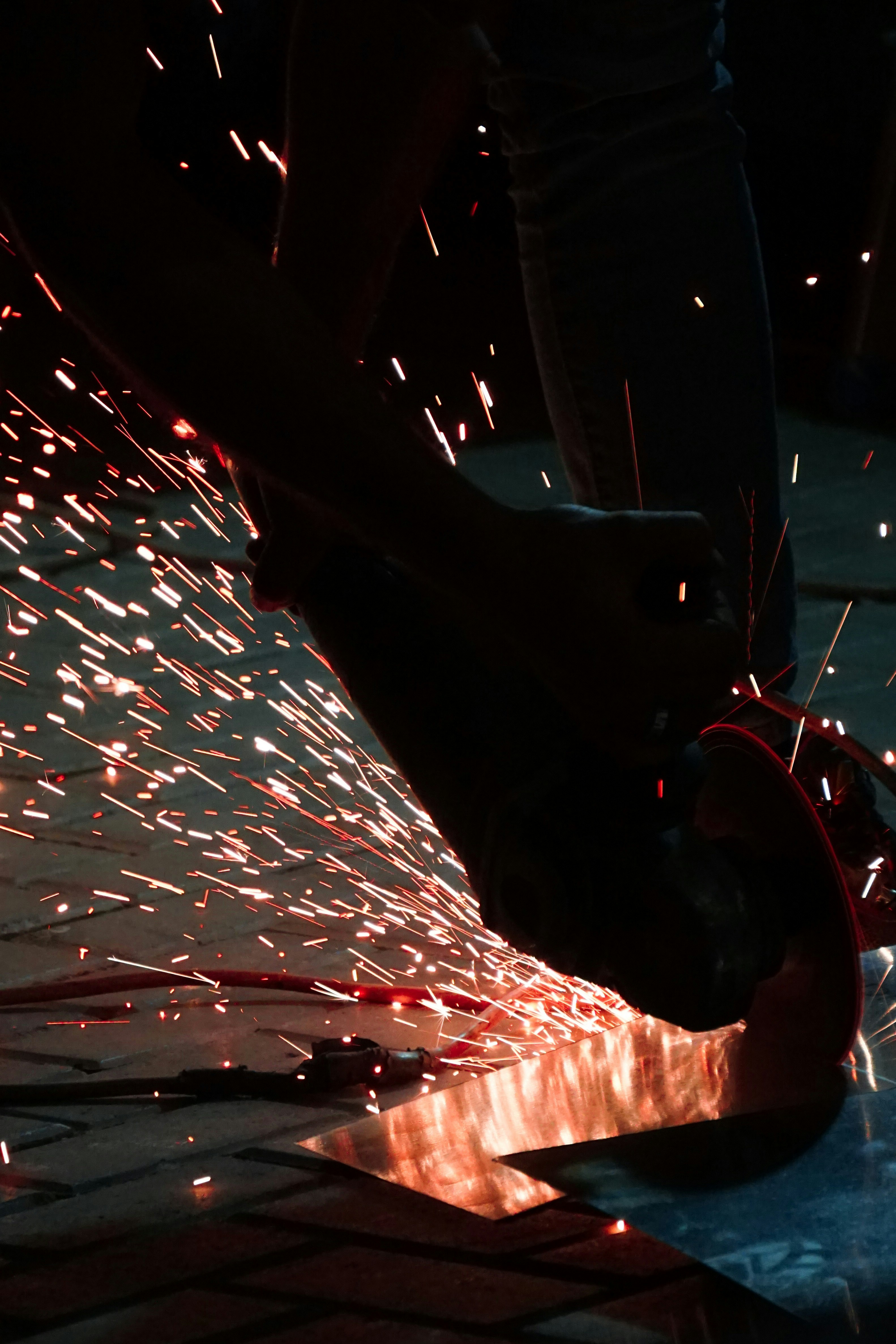 A craftsman skillfully operates a cutting tool, sending sparks flying against a reflective surface. The scene captures the intensity and precision of metalworking.