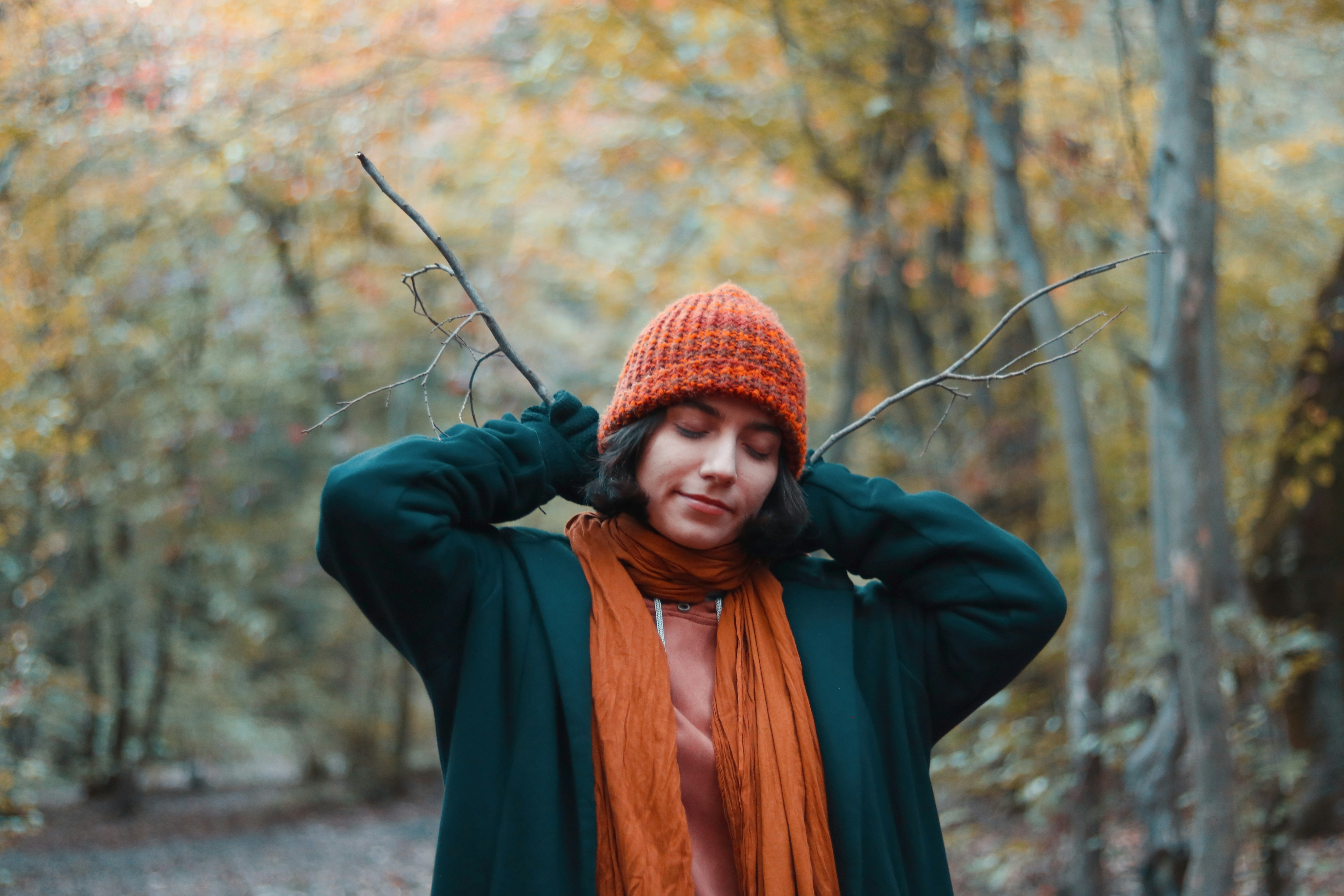 Person in a red hat and scarf enjoys a peaceful moment in a colorful autumn forest.