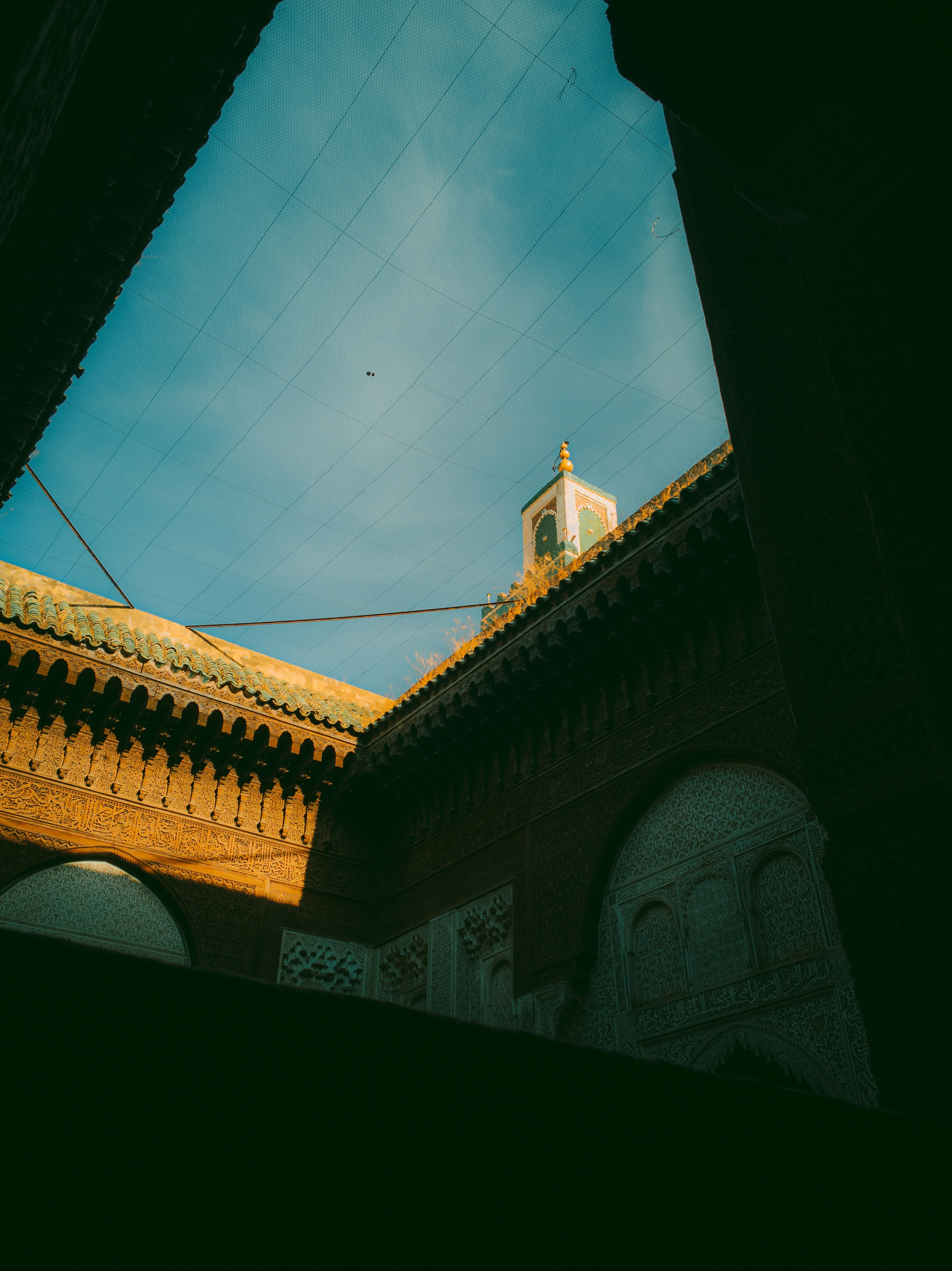 Azure sky framed by ornate arches and shadowed courtyard walls, with a distant minaret catching the light.