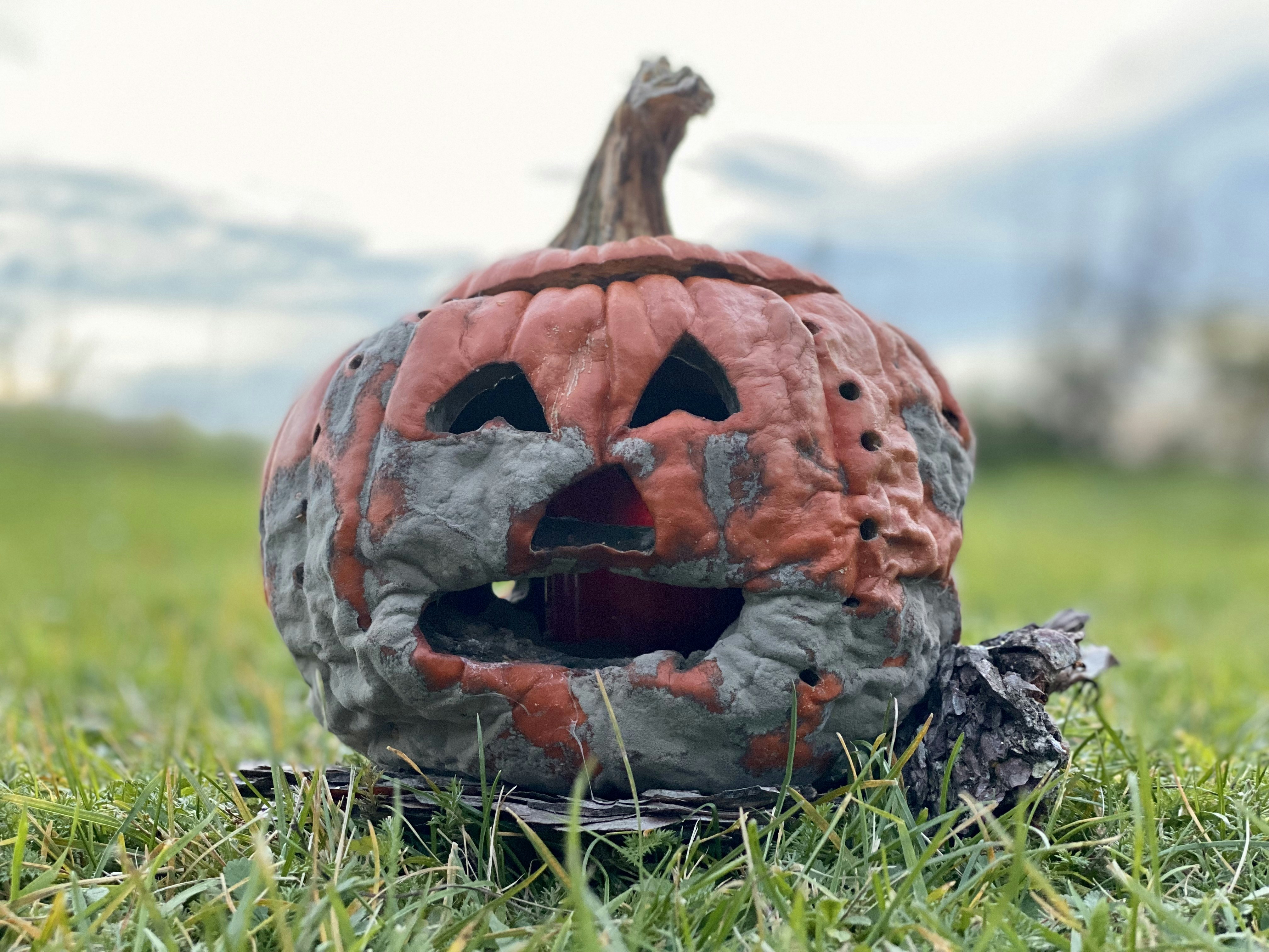 A weathered jack-o'-lantern with a cracked exterior sits on lush grass, embodying the remnants of Halloween festivities.
