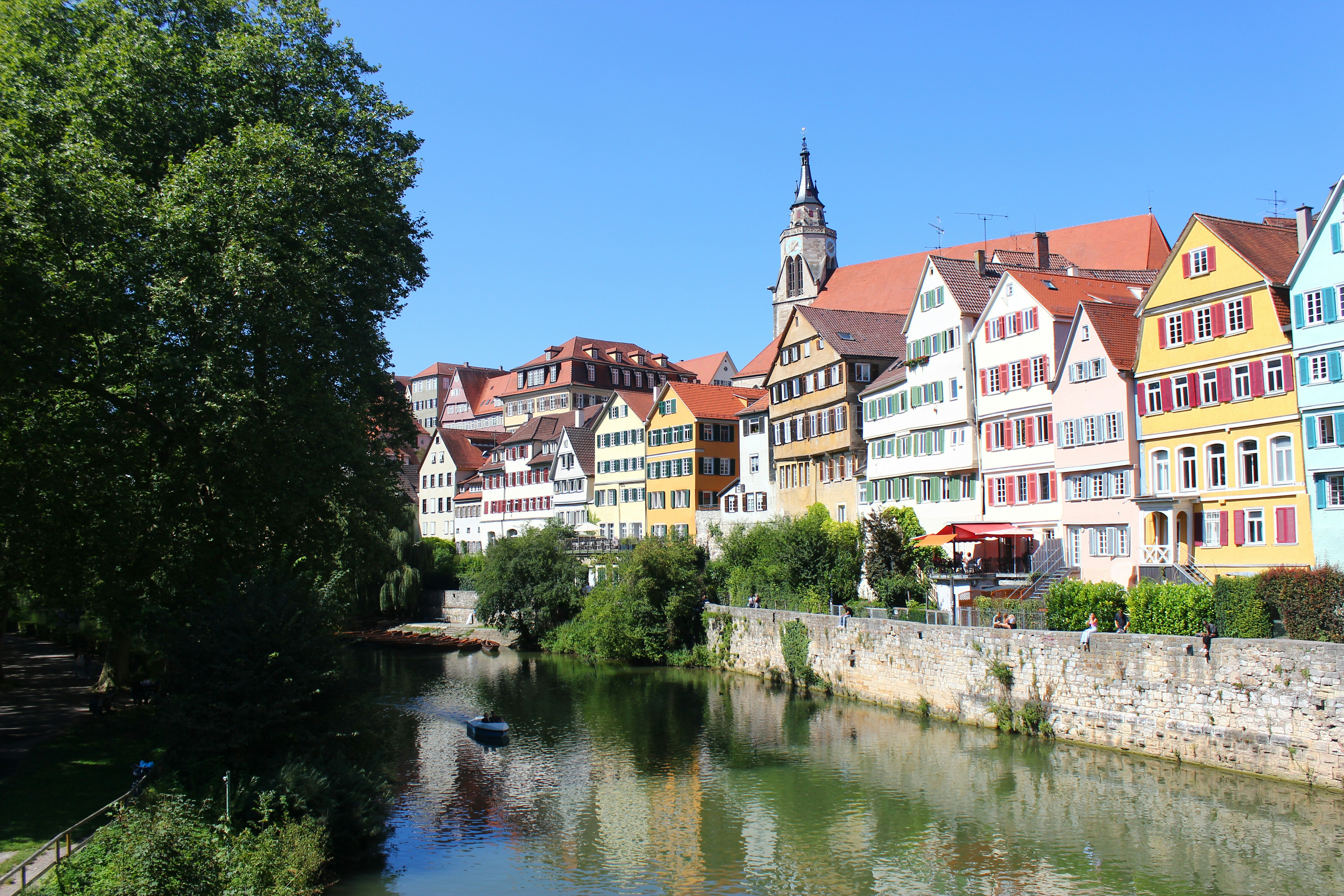 Colorful historic buildings line the Neckar River under a clear blue sky.