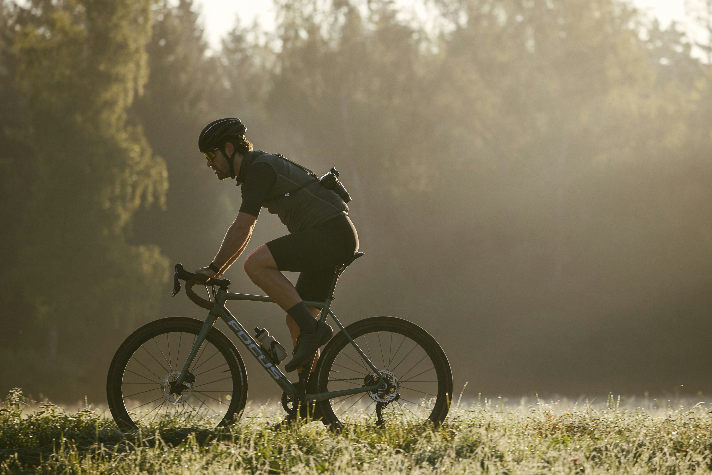 Cyclist navigating a dew-kissed meadow at dawn, surrounded by soft fog and tall trees.
