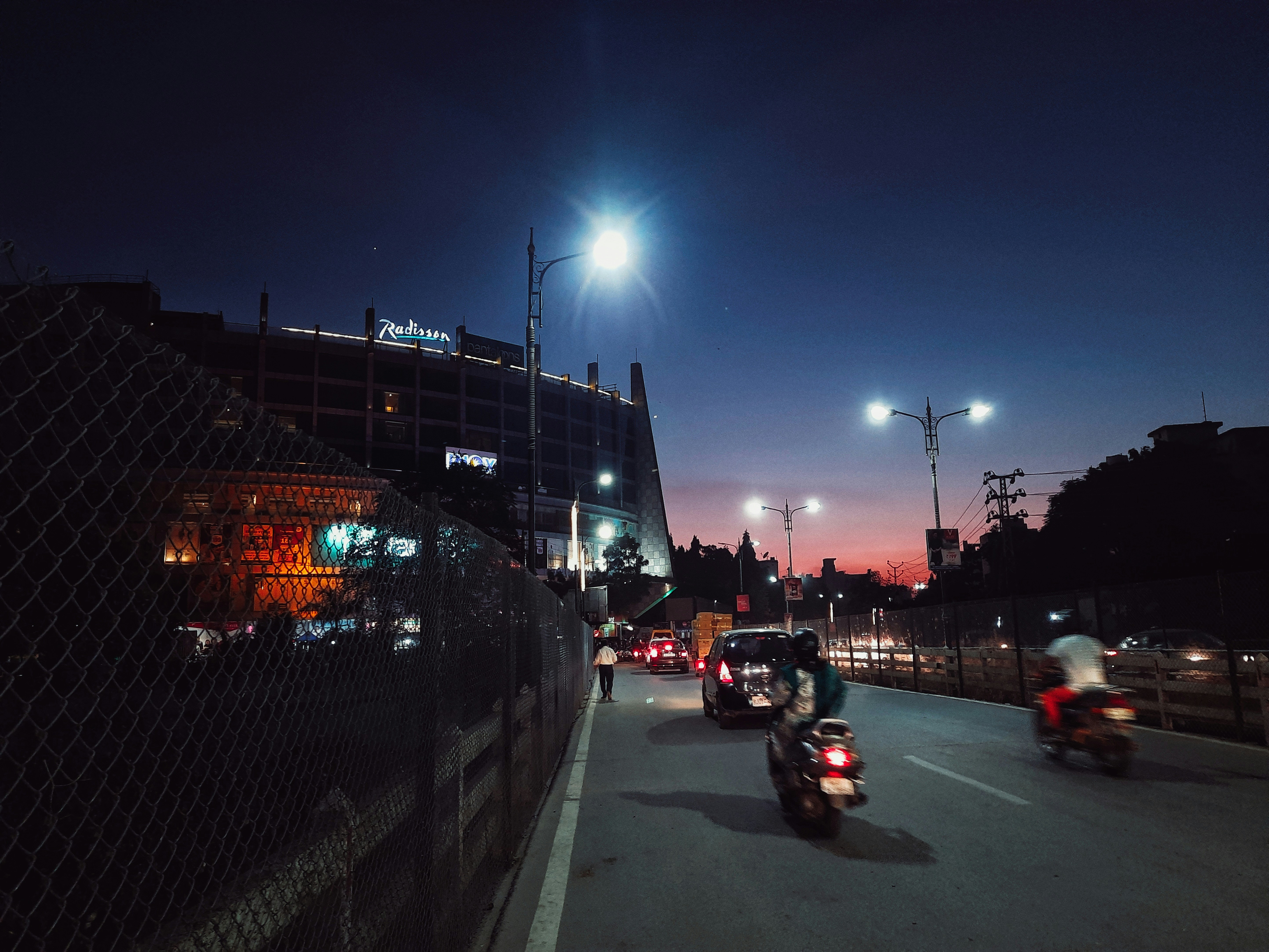 Busy street scene at twilight with vehicles and pedestrians, illuminated by streetlights. The Radisson hotel stands prominently in the background.