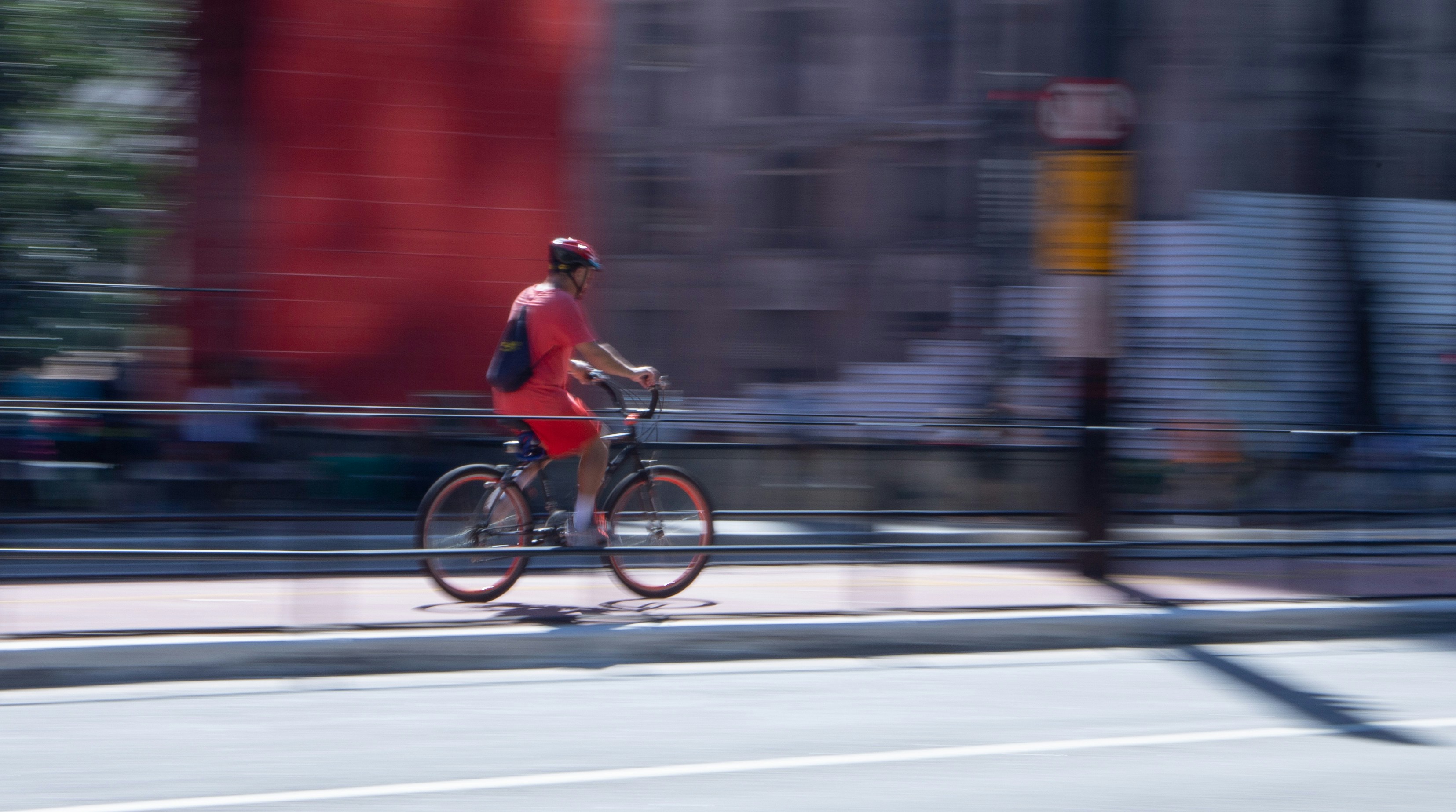Cyclist in red attire glides swiftly along a city street, with a blurred background suggesting speed.