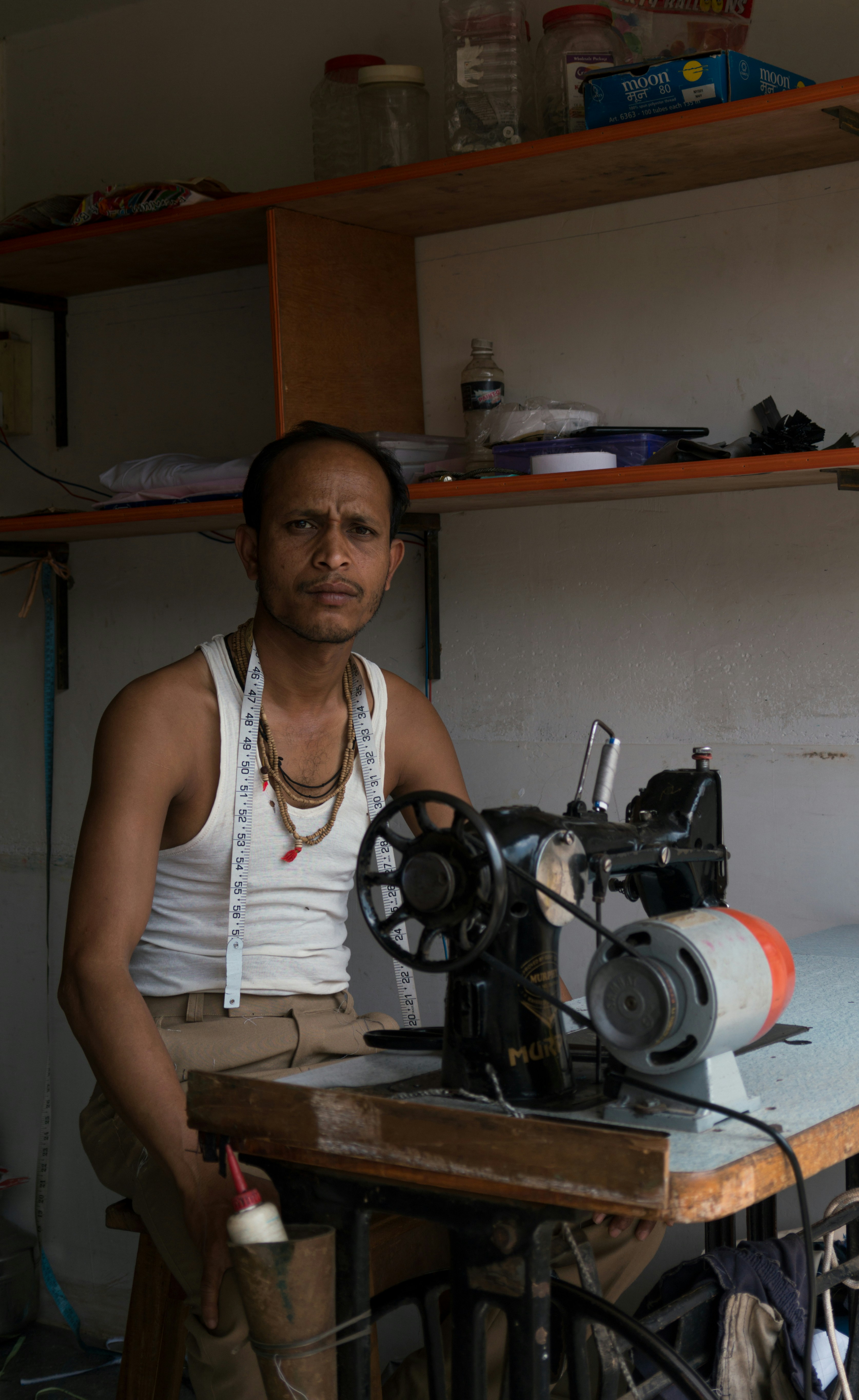 Our subject is a tailor, not posed but aware that he’s being photographed. Befuddled as a bird who flew into a house - he doesn’t know how to react. Should he present the best version of himself? Should he pose? A smile? A wink? Pout coquettishly like the girls he saw on the internet? It is this exact moment that’s captured on camera. The exact moment where he’s overwhelmed by the apparatus: the camera. Though being photographed is not new to him, I’ve caught him at his workplace wearing a banyan, I’ve caught without any ostentation, without a façade. He’s at his most raw state.