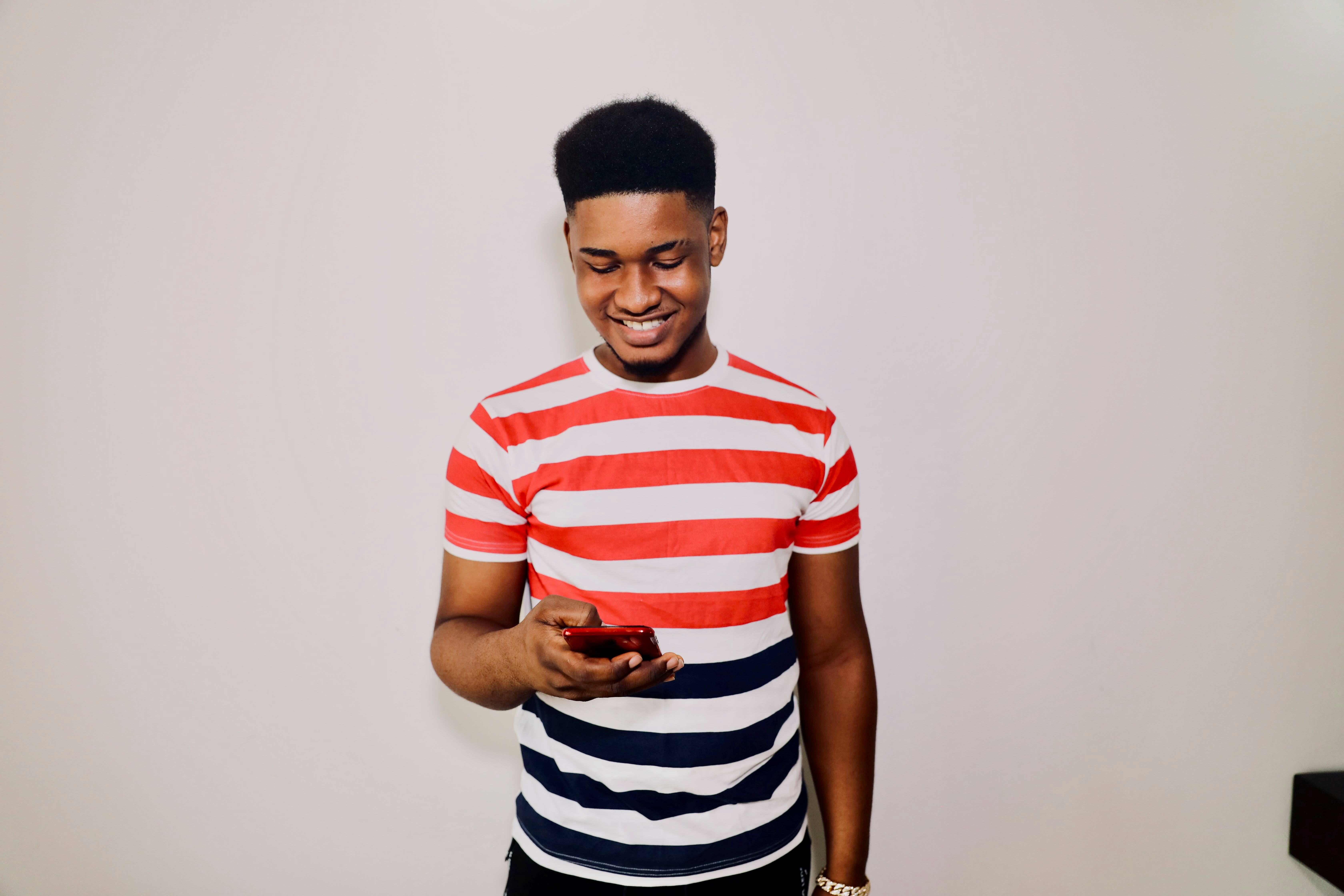 Young man in a striped shirt smiles while looking at his smartphone, set against a plain background.