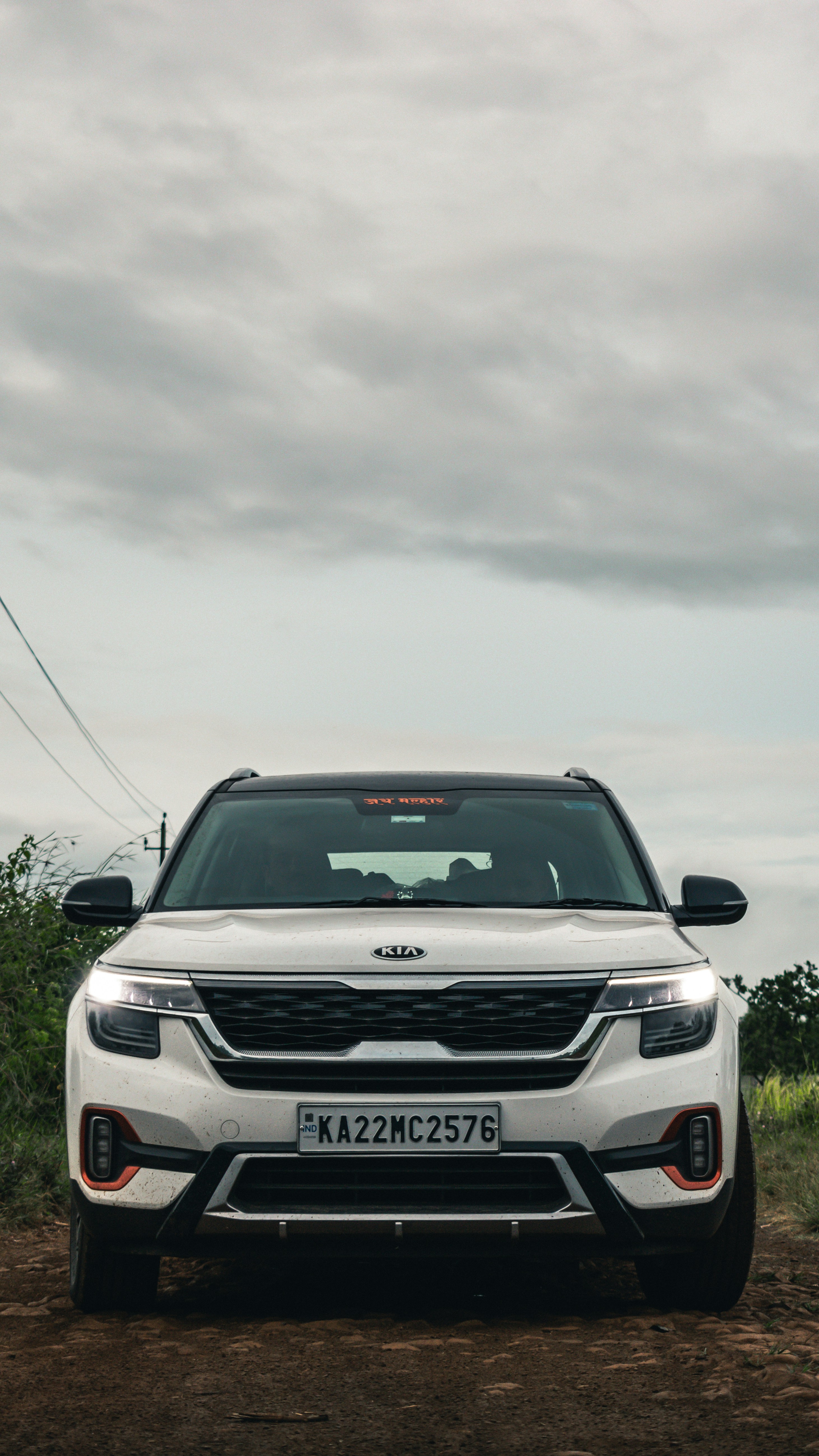 Front view of a sleek Kia SUV parked on a dirt road under a cloudy sky, showcasing its design and character.