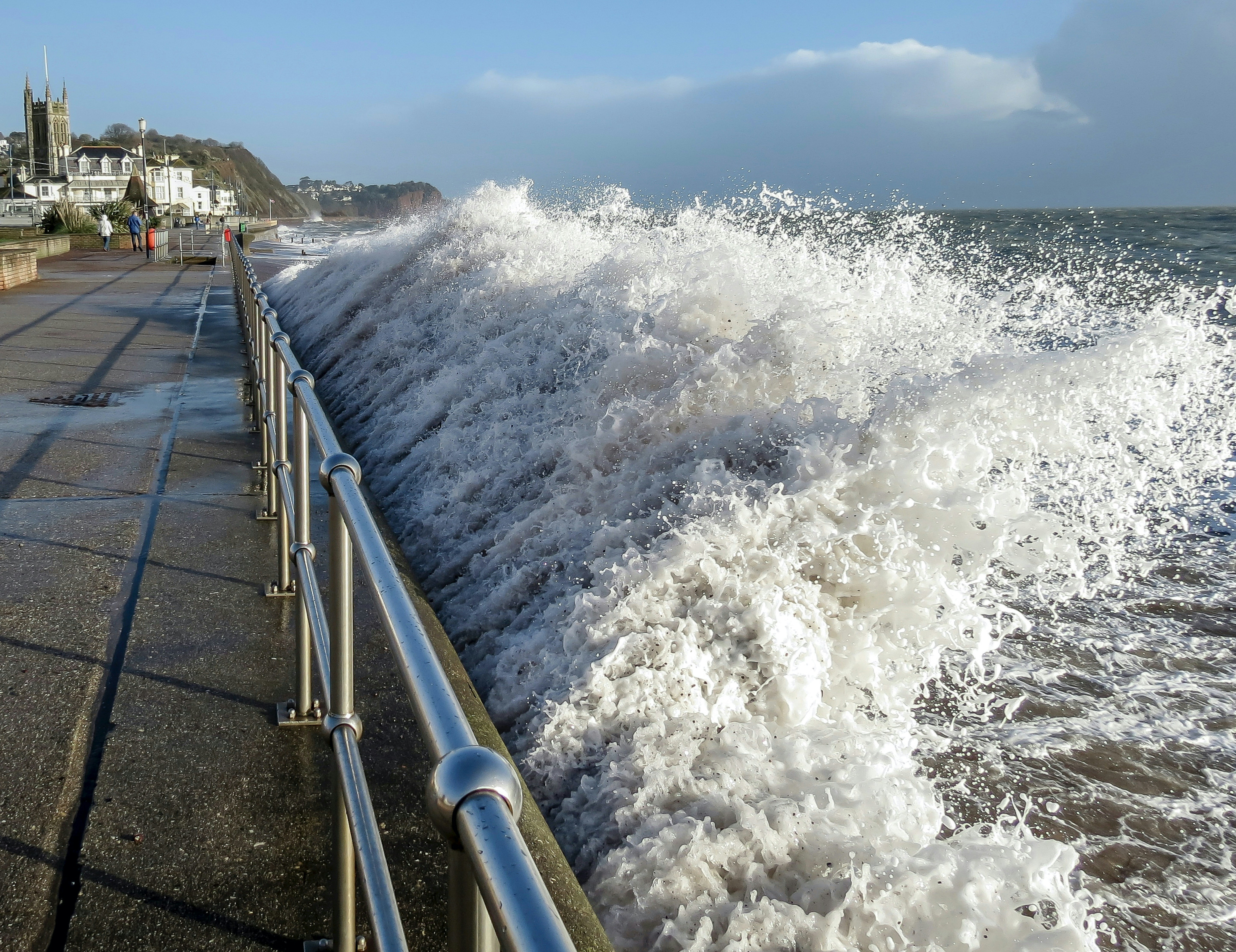 A large wave crashing over a metal railing next to the ocean photo ...