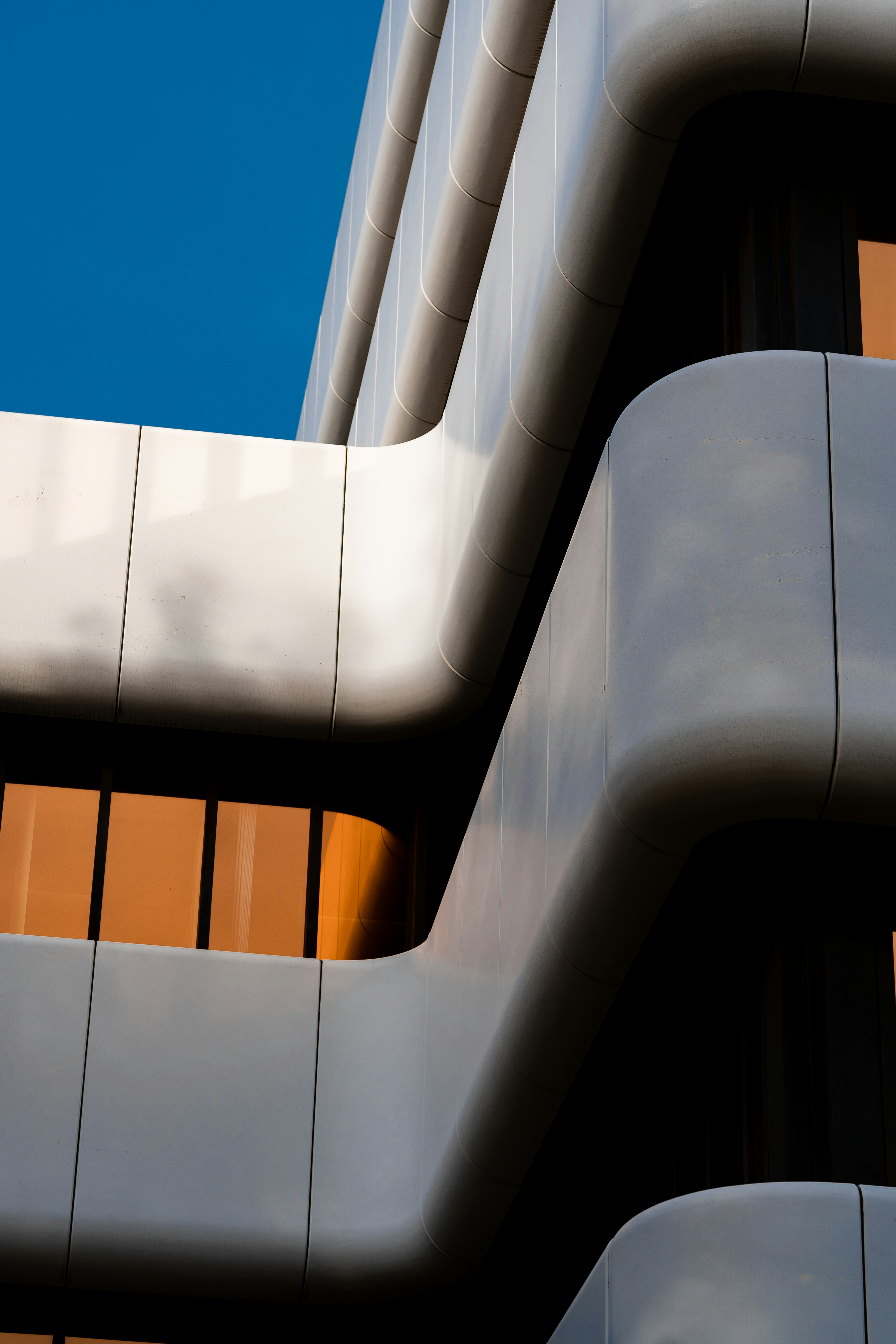 Abstract view of a contemporary building showcasing smooth curves and reflective surfaces against a clear blue sky.
