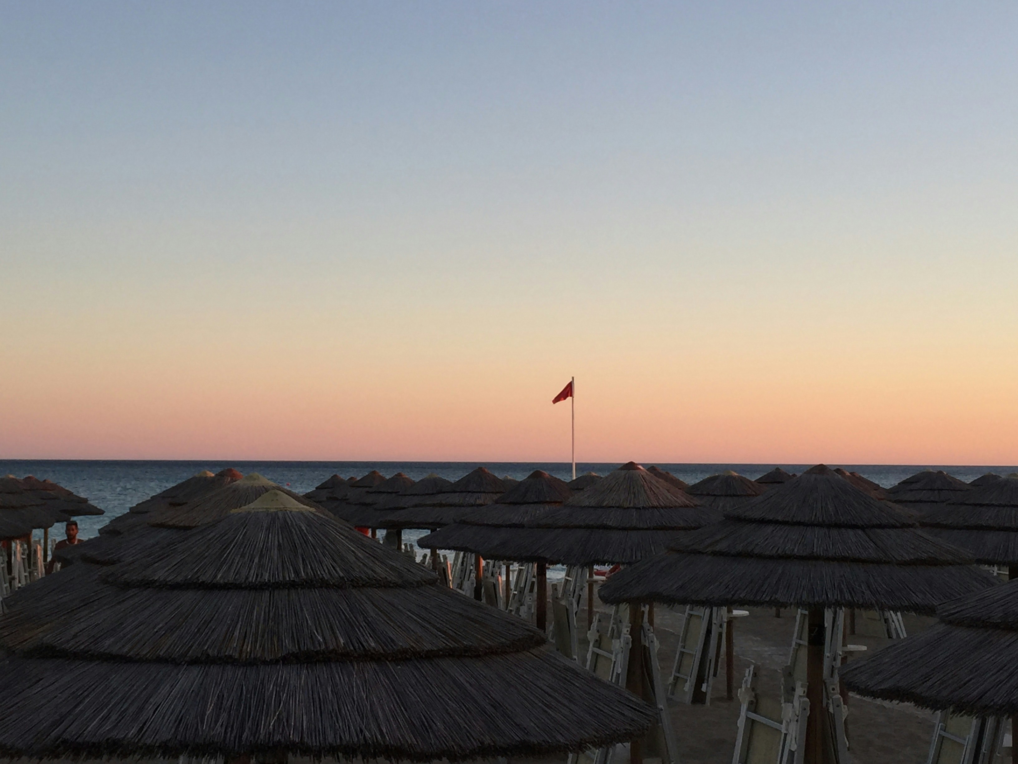 Rows of beach umbrellas silhouetted against a pastel sunset sky by the sea.
