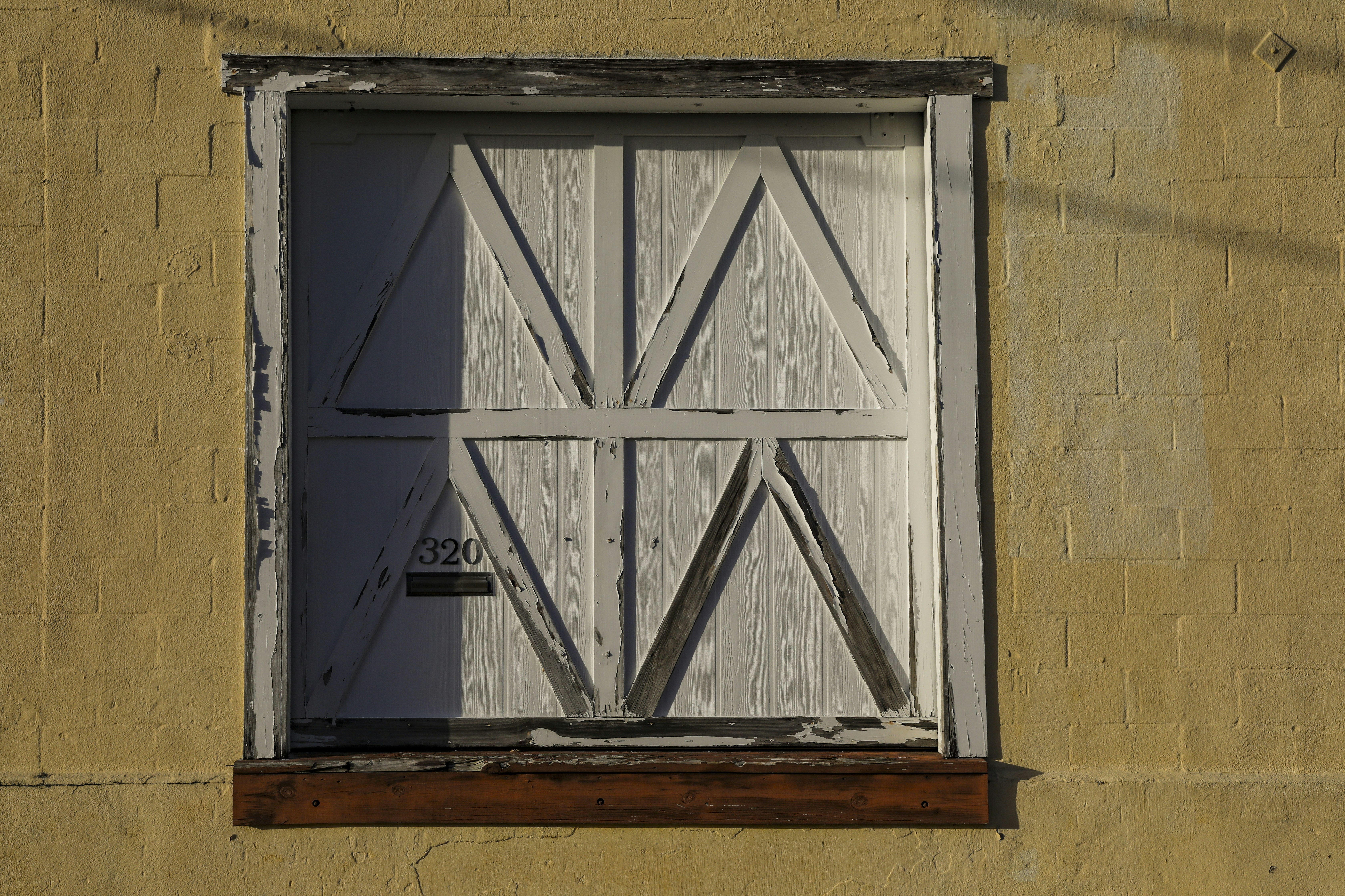 A rustic wooden window with geometric patterns casts shadows on a sunlit wall.