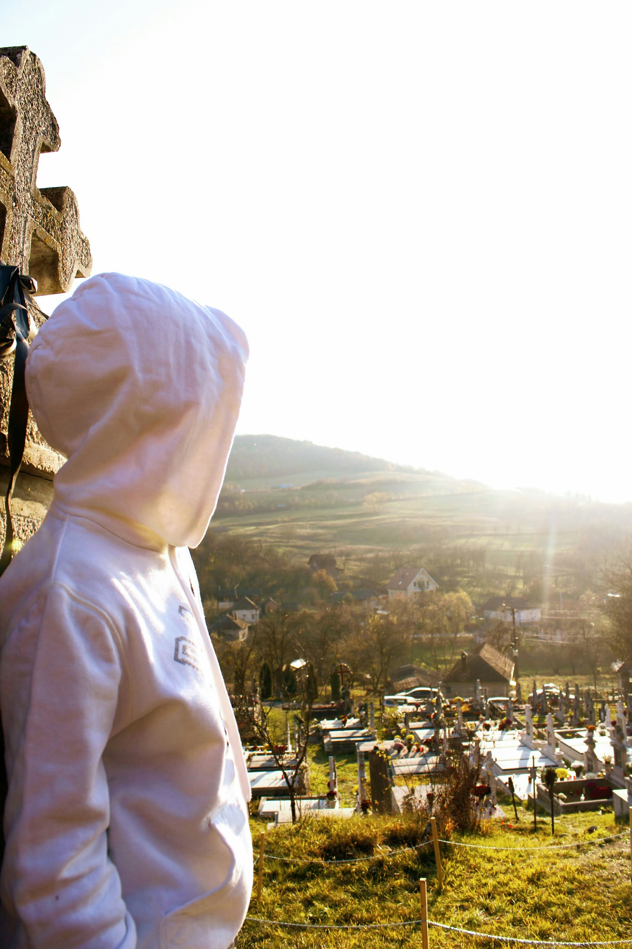 Hooded Figure on a Sunlit Hillside Overlooking a Quiet Cemetery