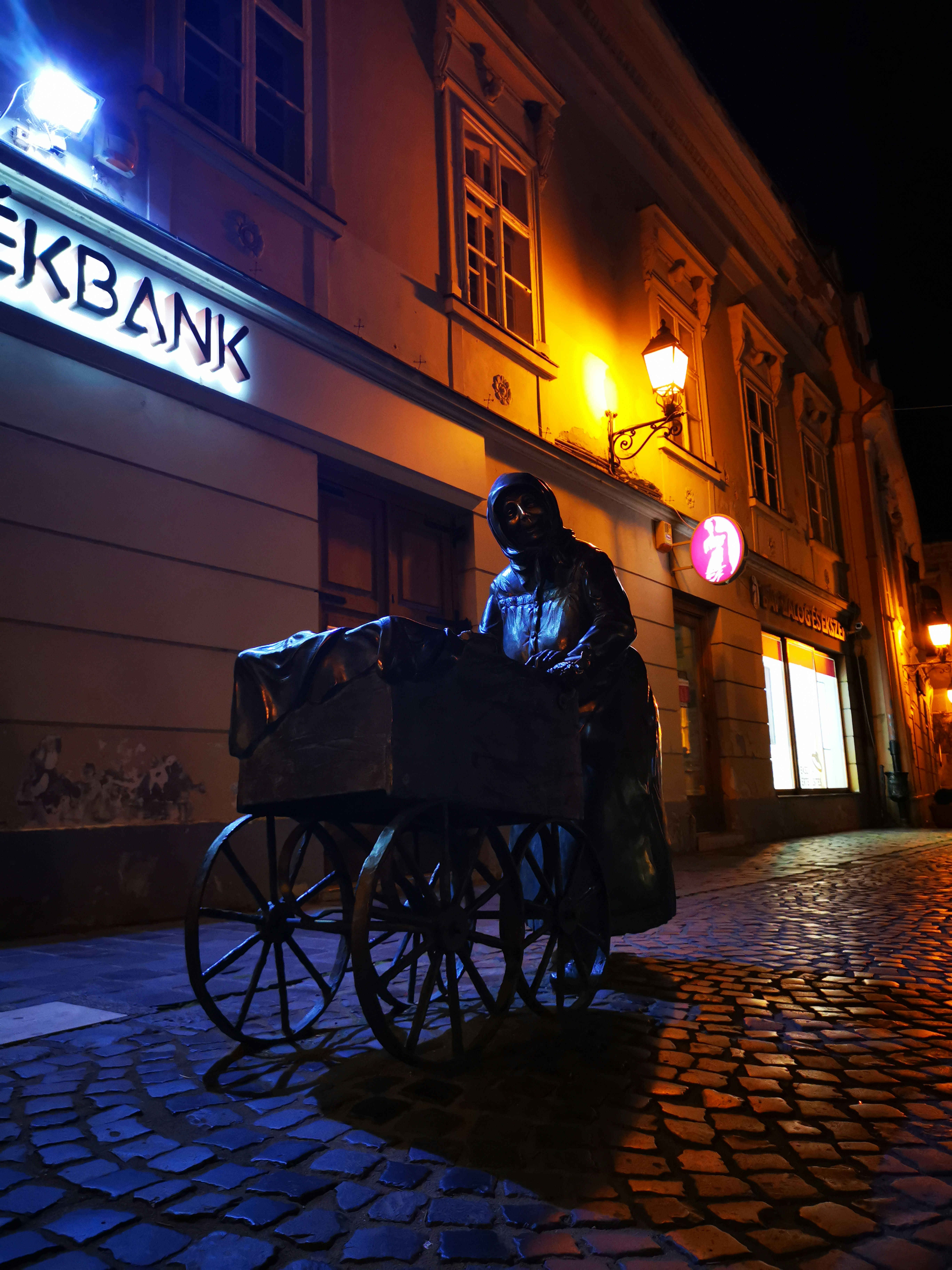 Silhouette of a person with a cart on a dimly lit cobblestone street at night.