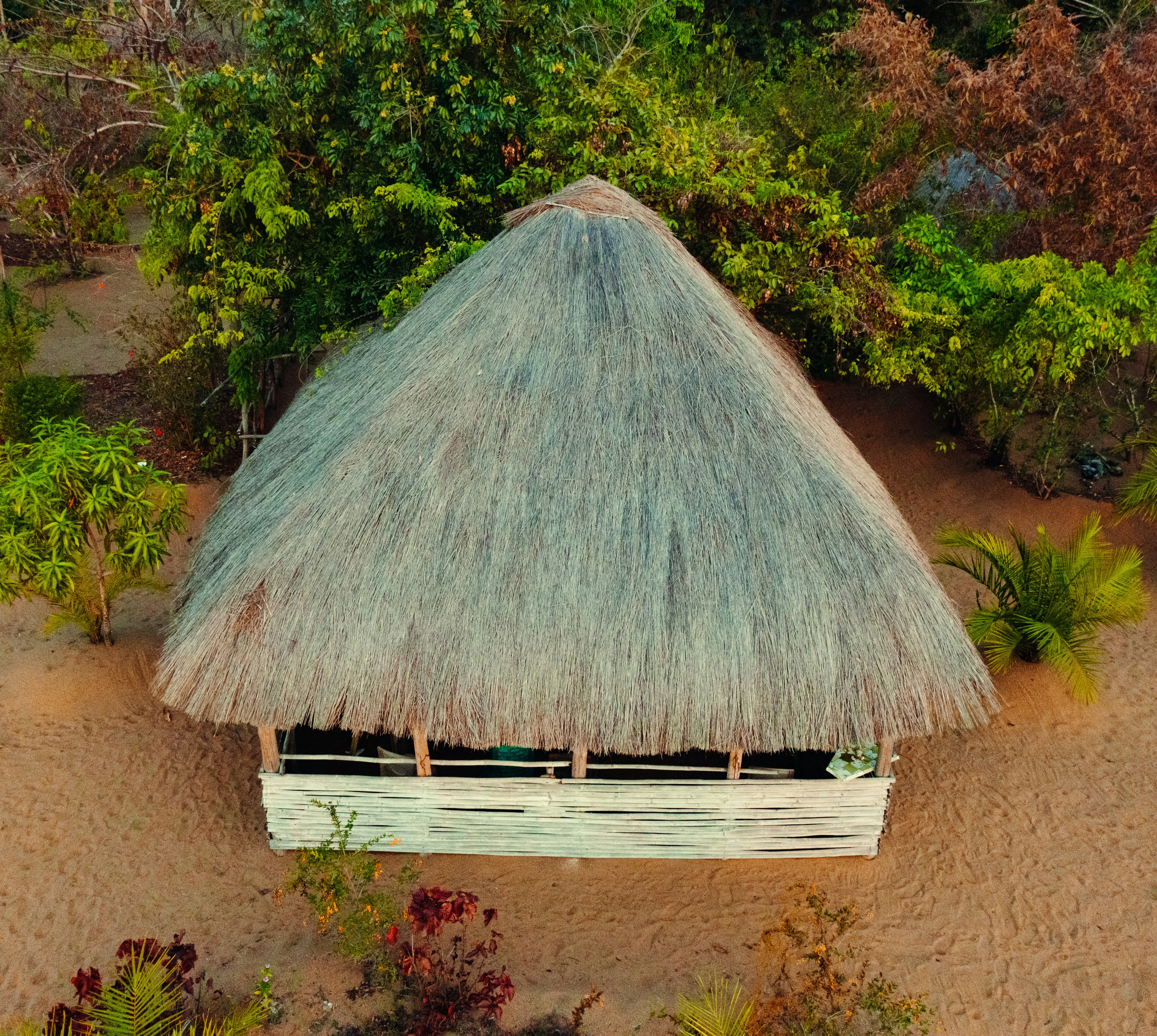 A traditional thatched-roof structure surrounded by lush greenery and sandy terrain, showcasing a harmonious blend with the natural environment.