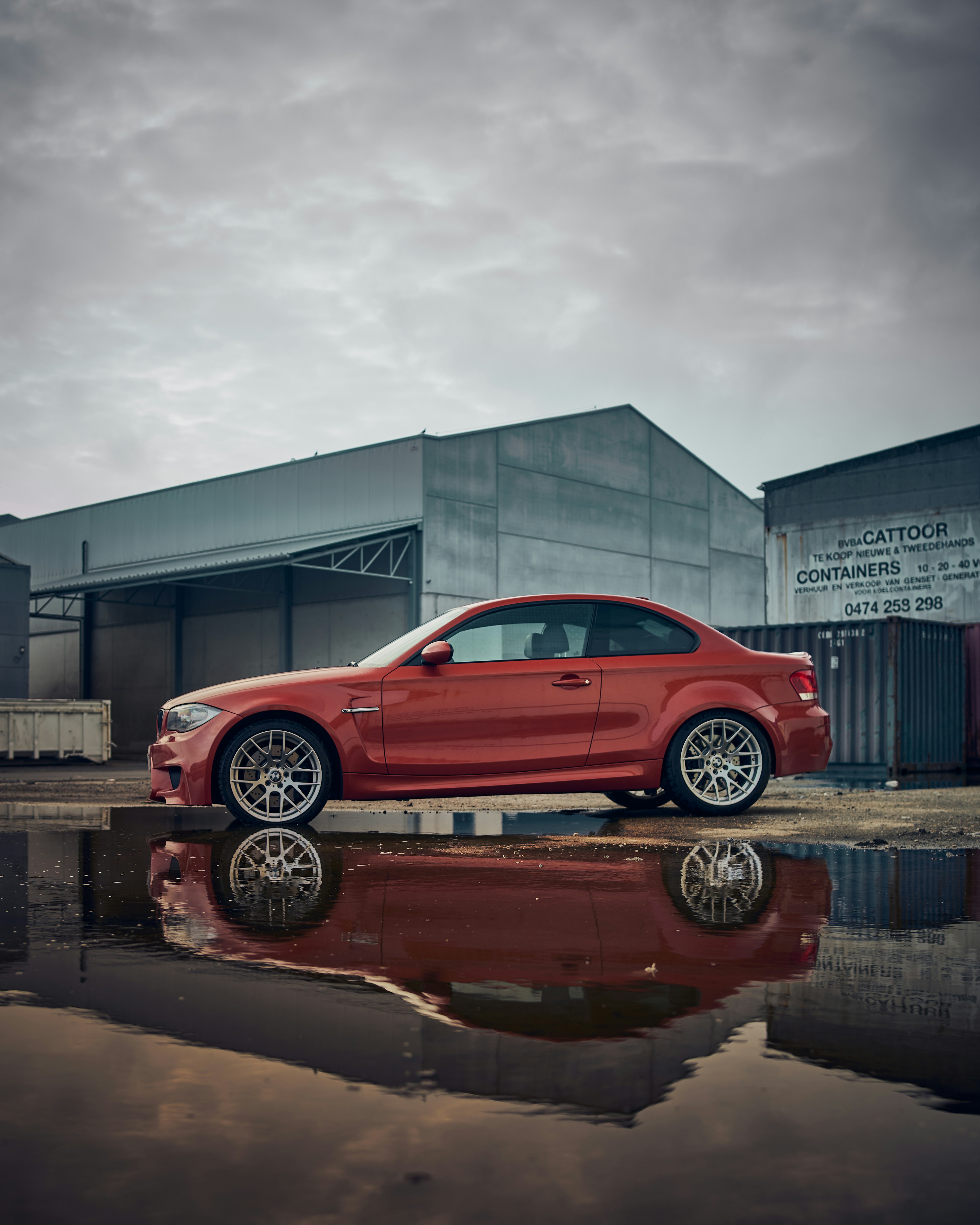 Red Velocity: A Citrus-red Coupe Reflected in Industrial Stillness