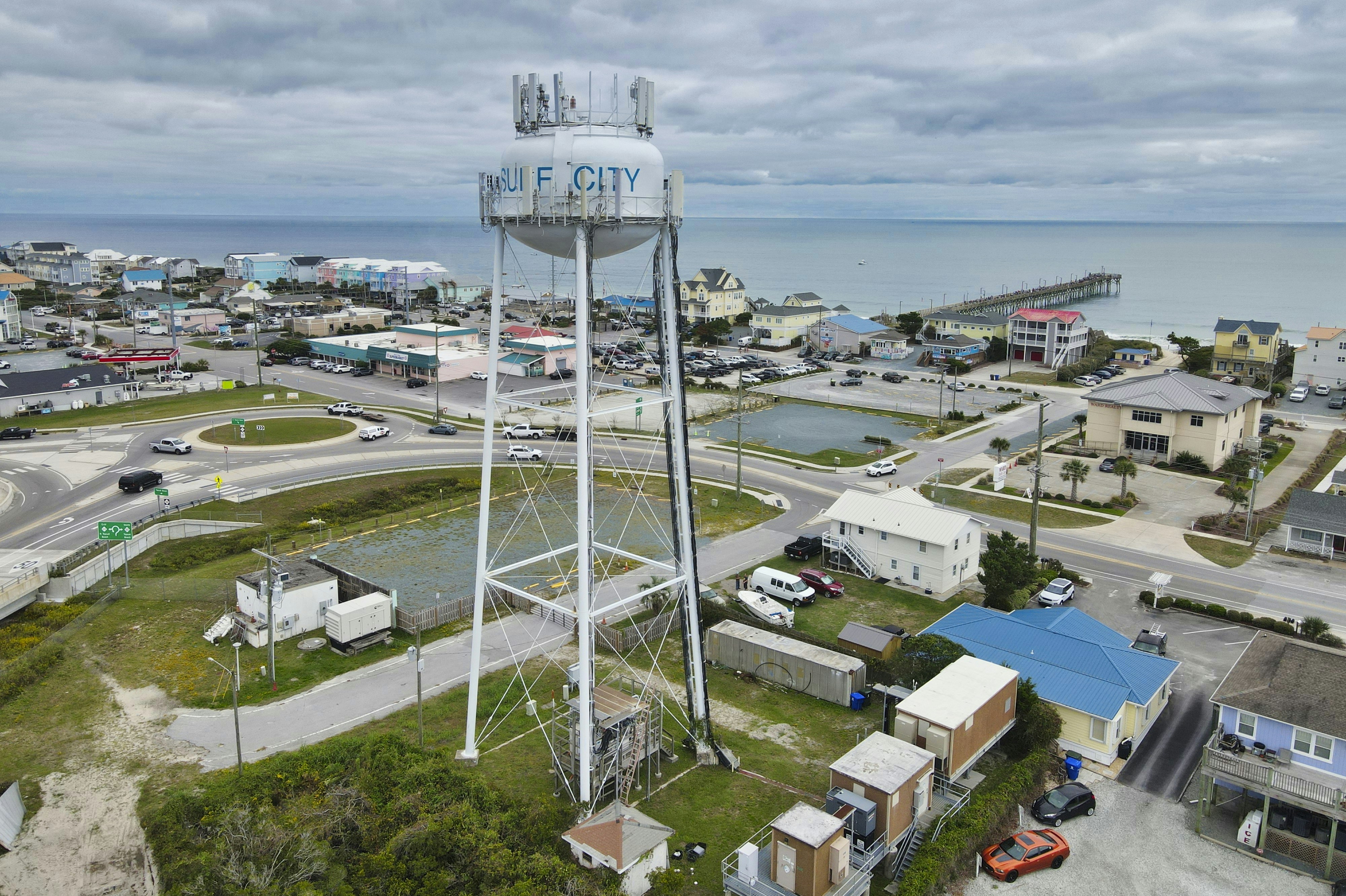 Water tower stands prominently amidst a coastal town, showcasing a blend of residential and commercial structures with a serene ocean backdrop.