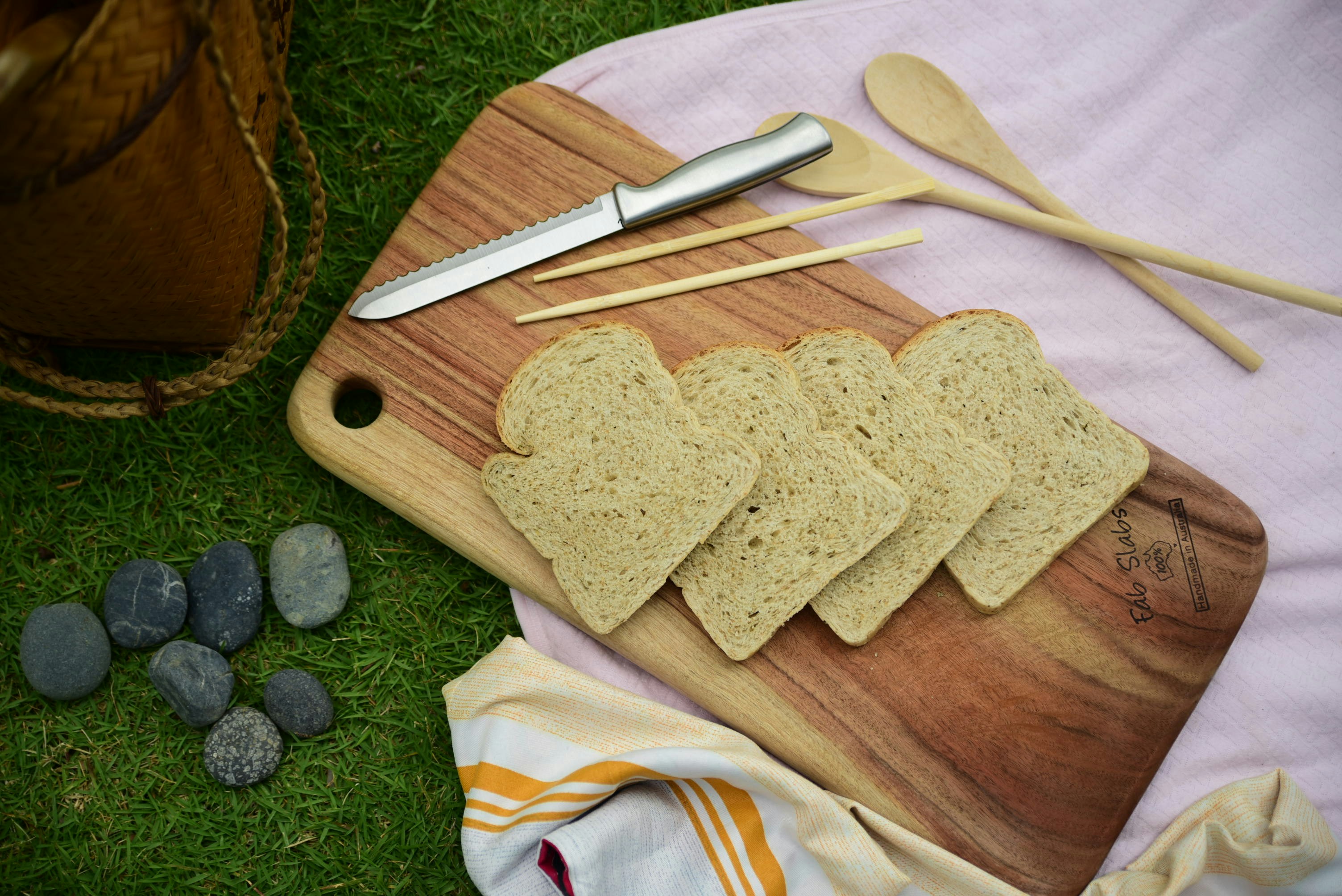 Crusty bread slices rest on a sunlit wooden board in a grassy picnic scene