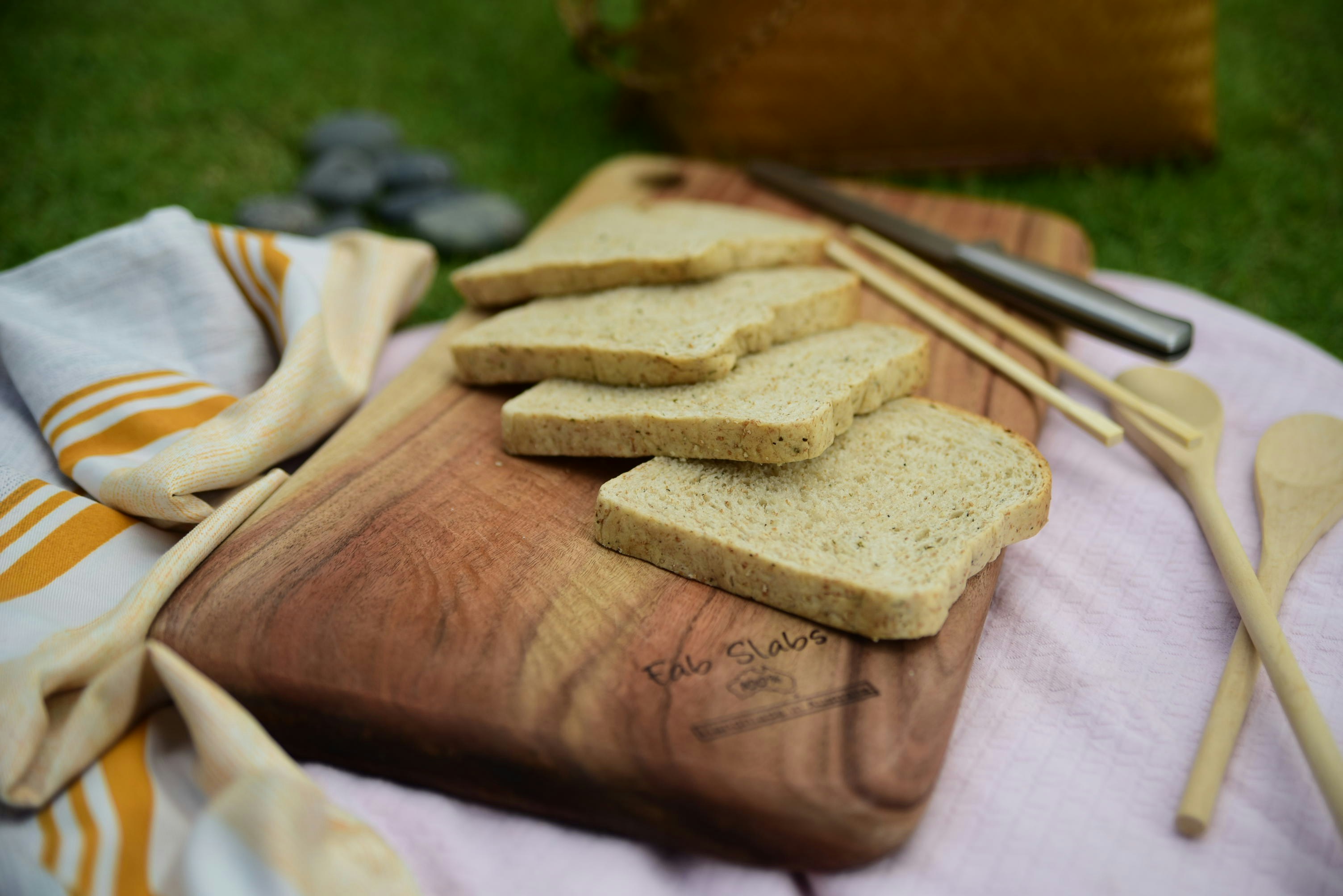 Freshly sliced bread arranged on a wooden cutting board, accompanied by utensils and a soft cloth, set against a natural backdrop.