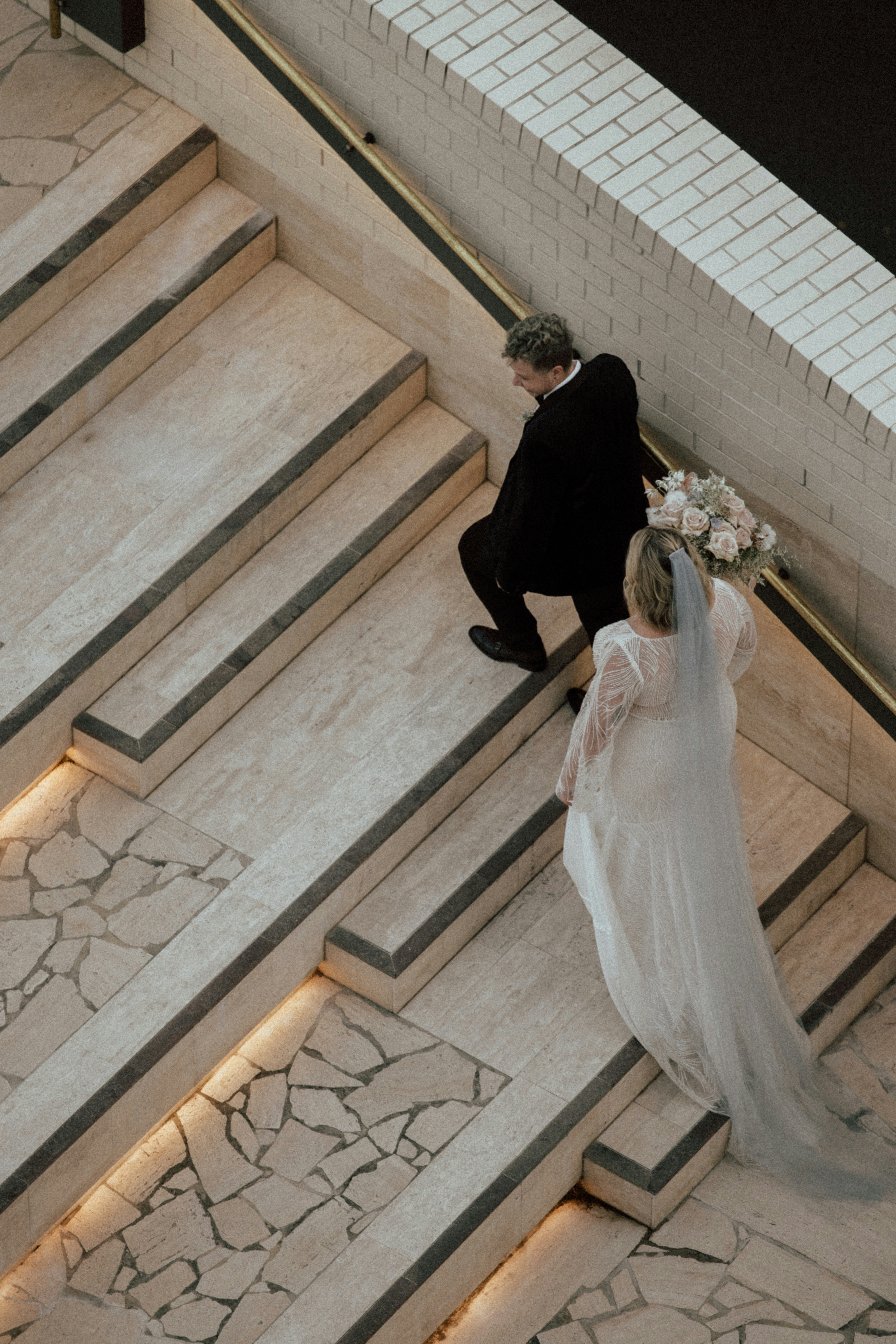 Staircase Vows: Bride and Groom Ascend Marble Steps Under Warm Glow