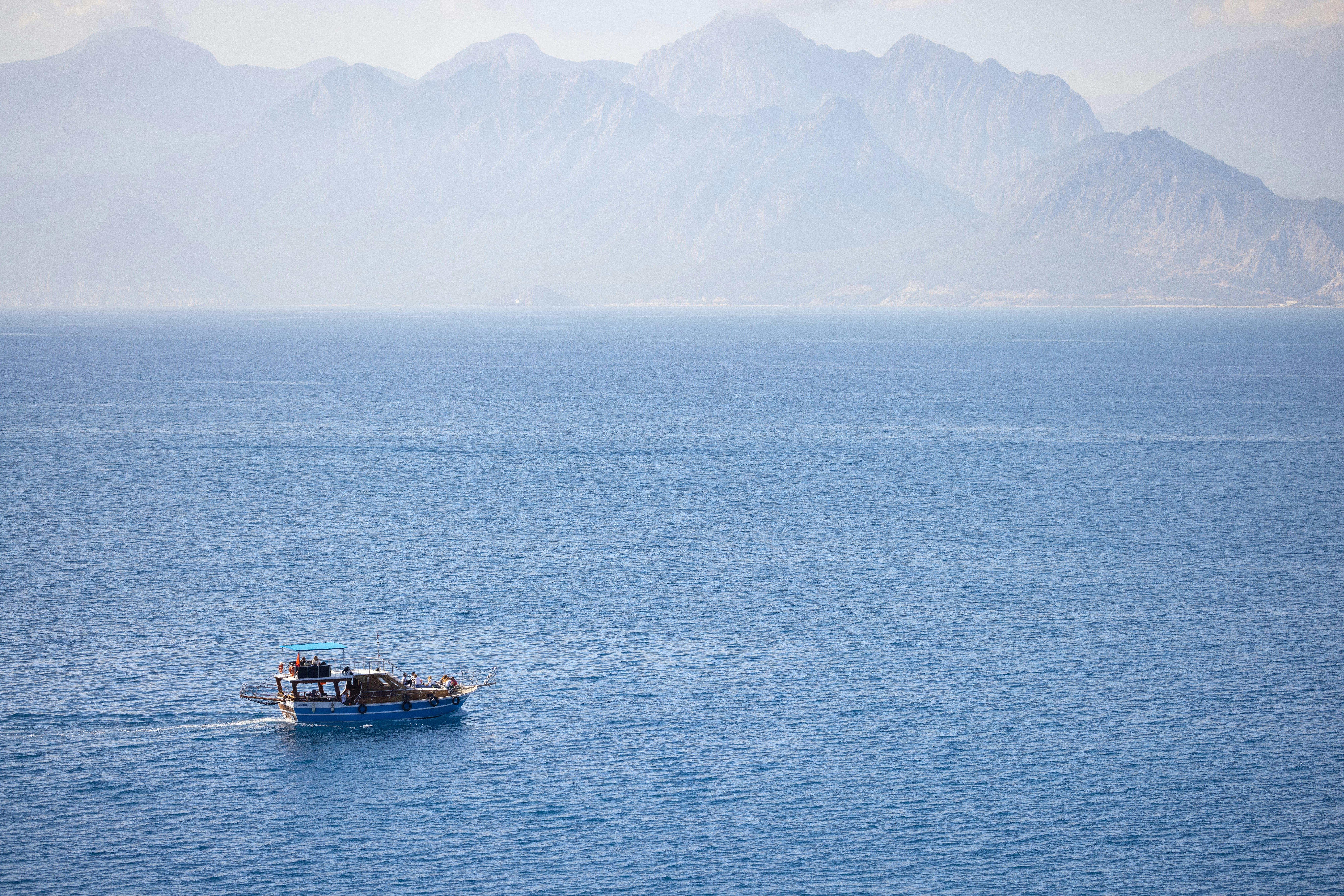 Fishing boat gliding across tranquil blue waters with distant mountains silhouetted against the sky.
